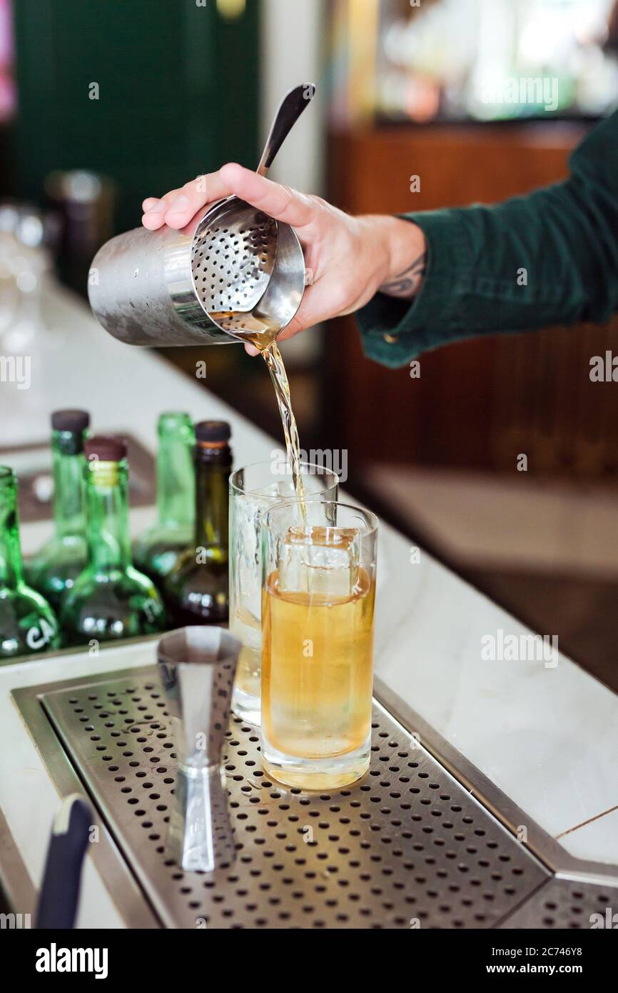 Bartender making a cocktail at the bar: pouring a drink from a shaker ...