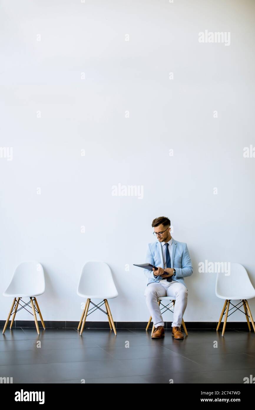 Young man sitting at chair in the waiting room with a folder in hand ...