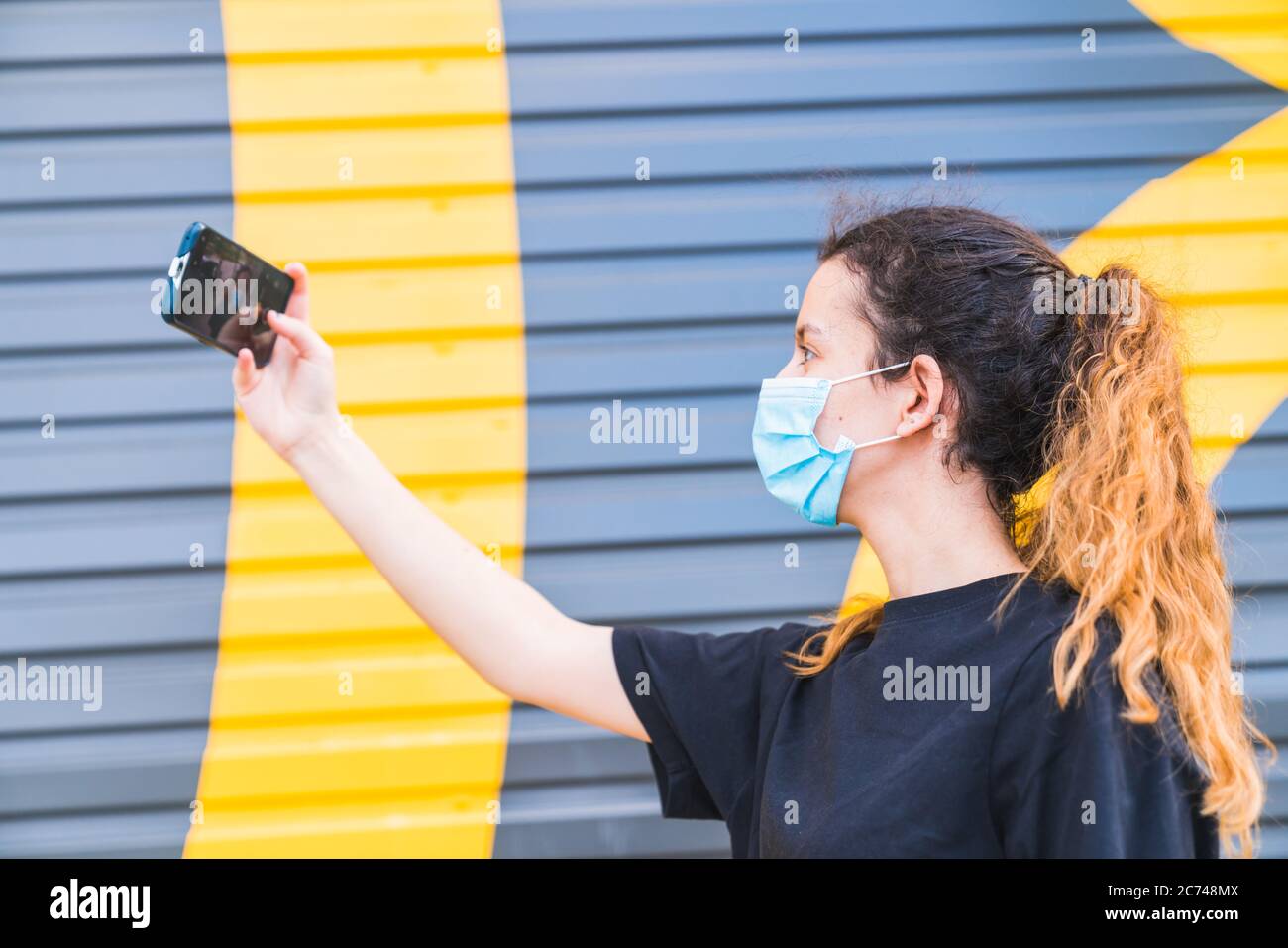 Teenager making a selfie on the street wearing a mask. Young woman ...