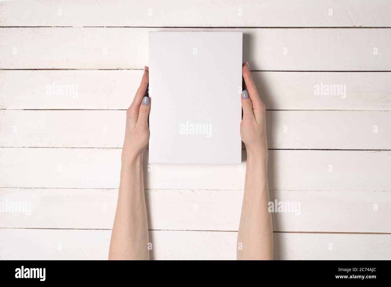 White rectangular box in female hands. Top view. White table on the ...