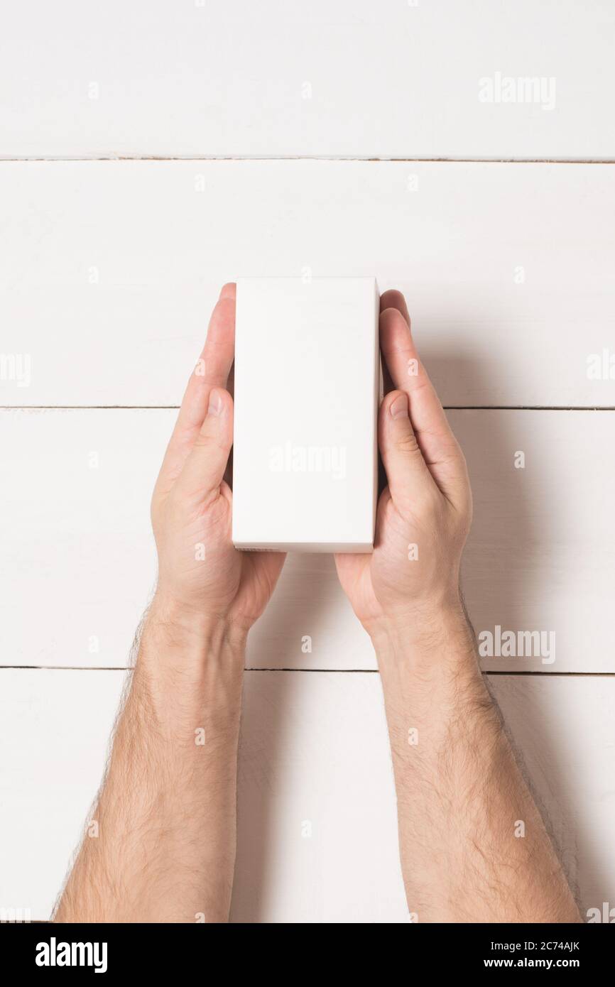 White rectangular box in male hands. Top view. White table on the ...