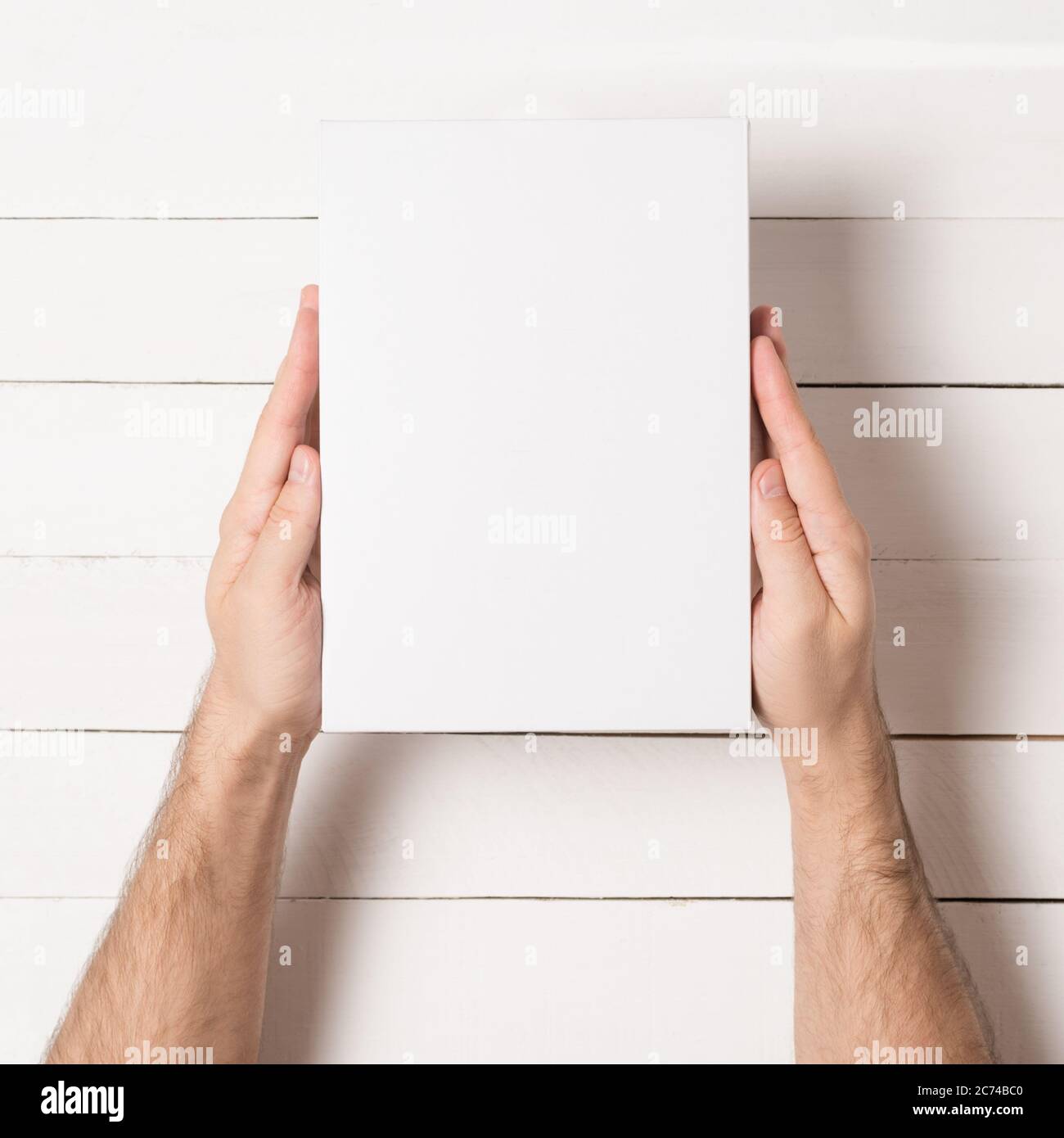 White rectangular box in male hands. Top view. White table on the ...