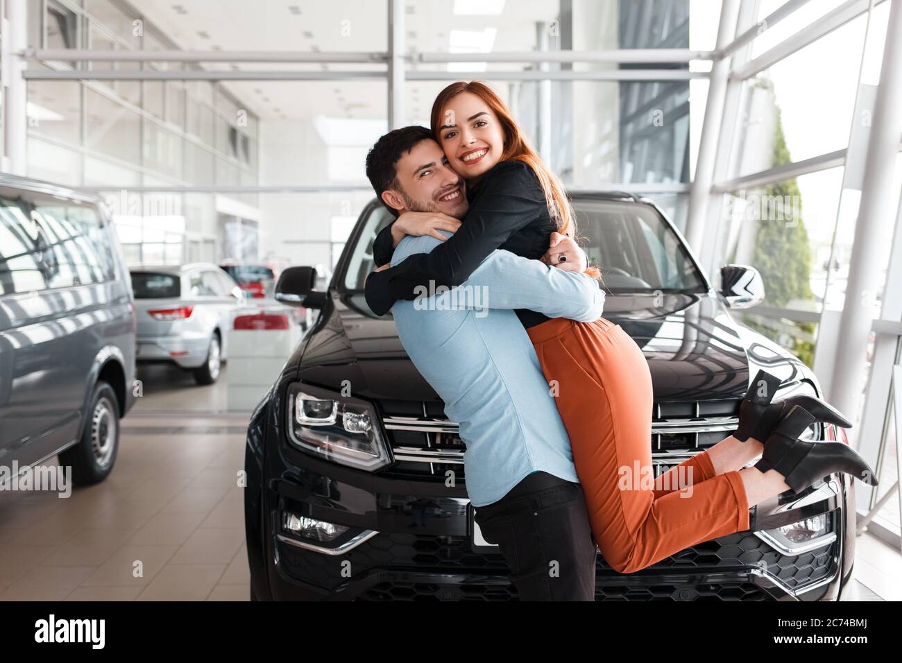 Guy hugs his girlfriend in a car dealership on the background of a ...