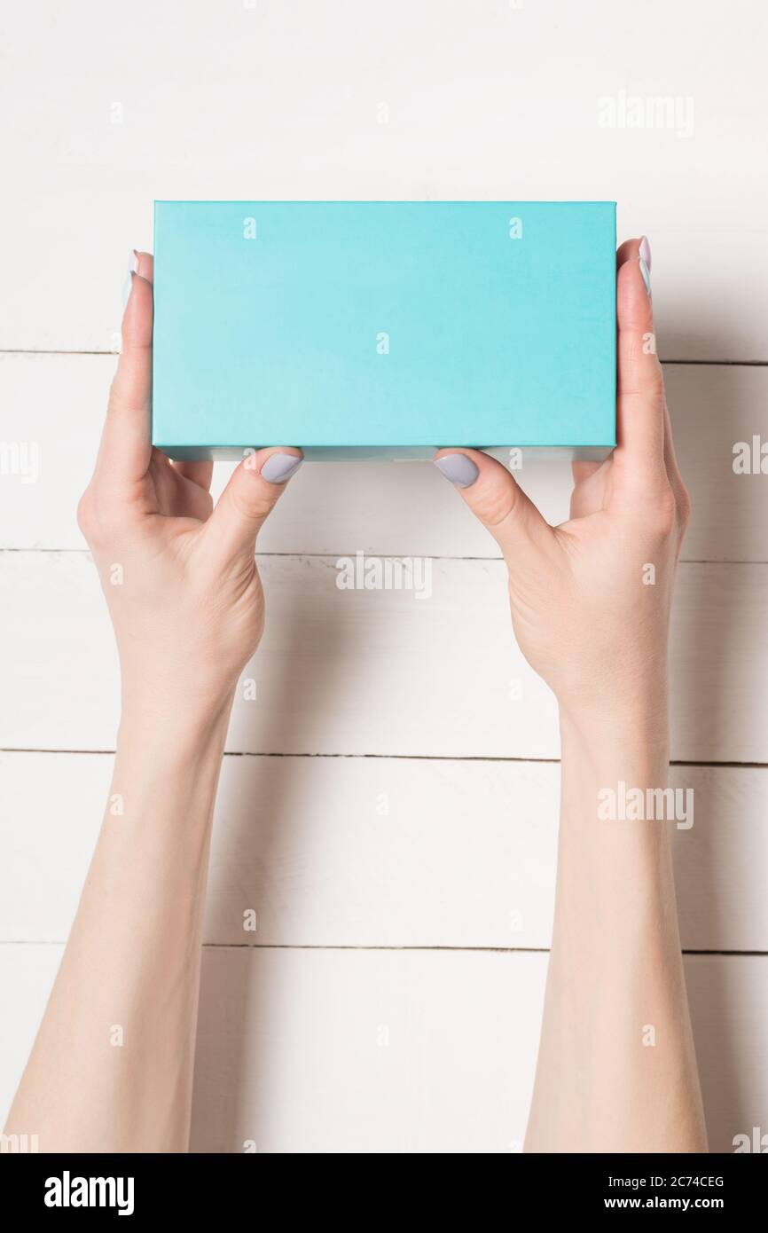 Rectangular turquoise box in female hands. Top view. White table on the ...