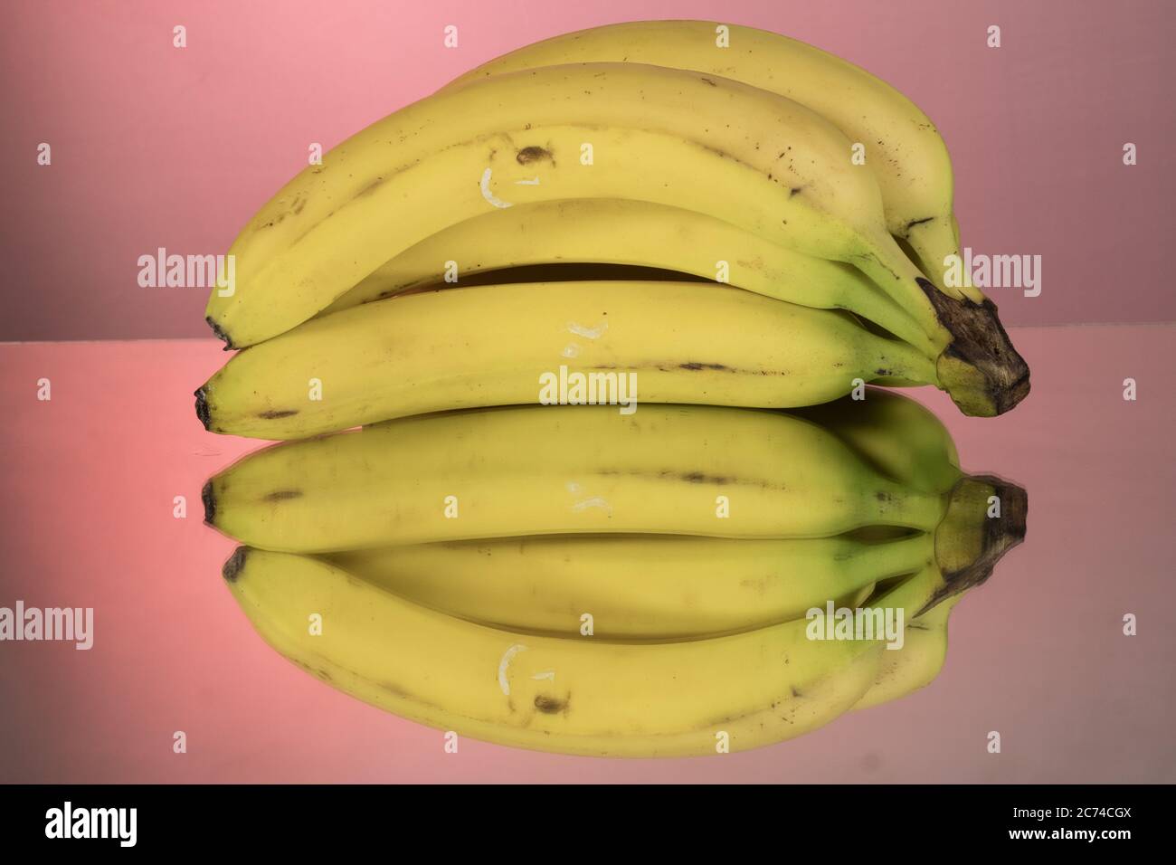 A bunch of bananas on mirroring table on mirror red background with ...