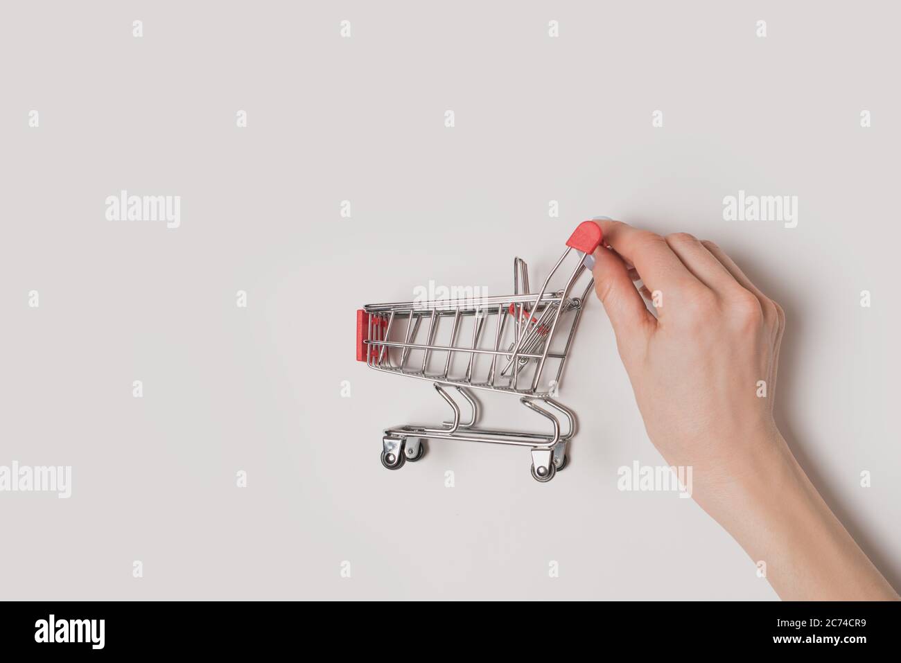 Small red metal shopping trolley in a female hand isolate on a light ...