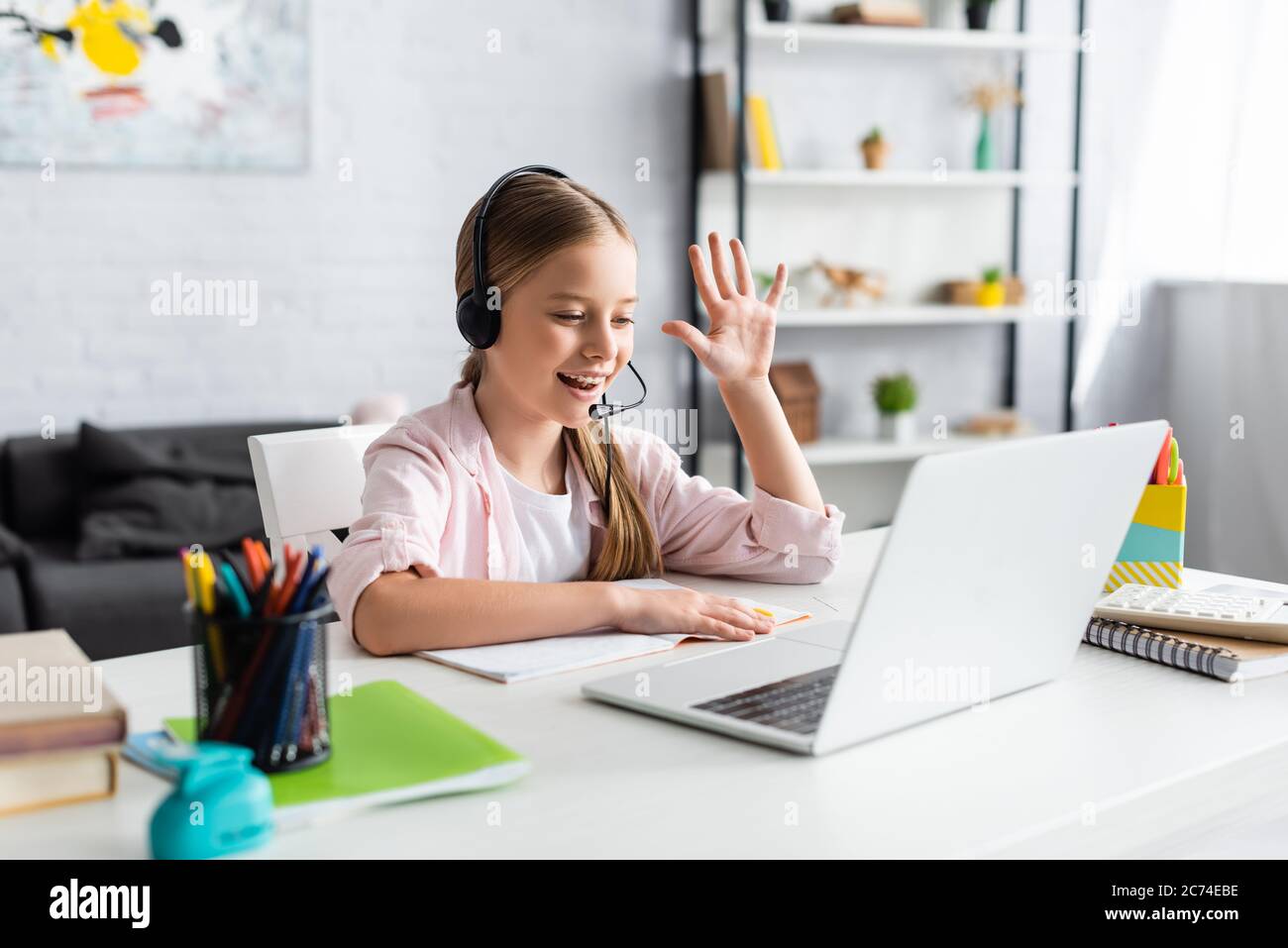 Selective focus of positive kid in headset waving hand during webinar ...