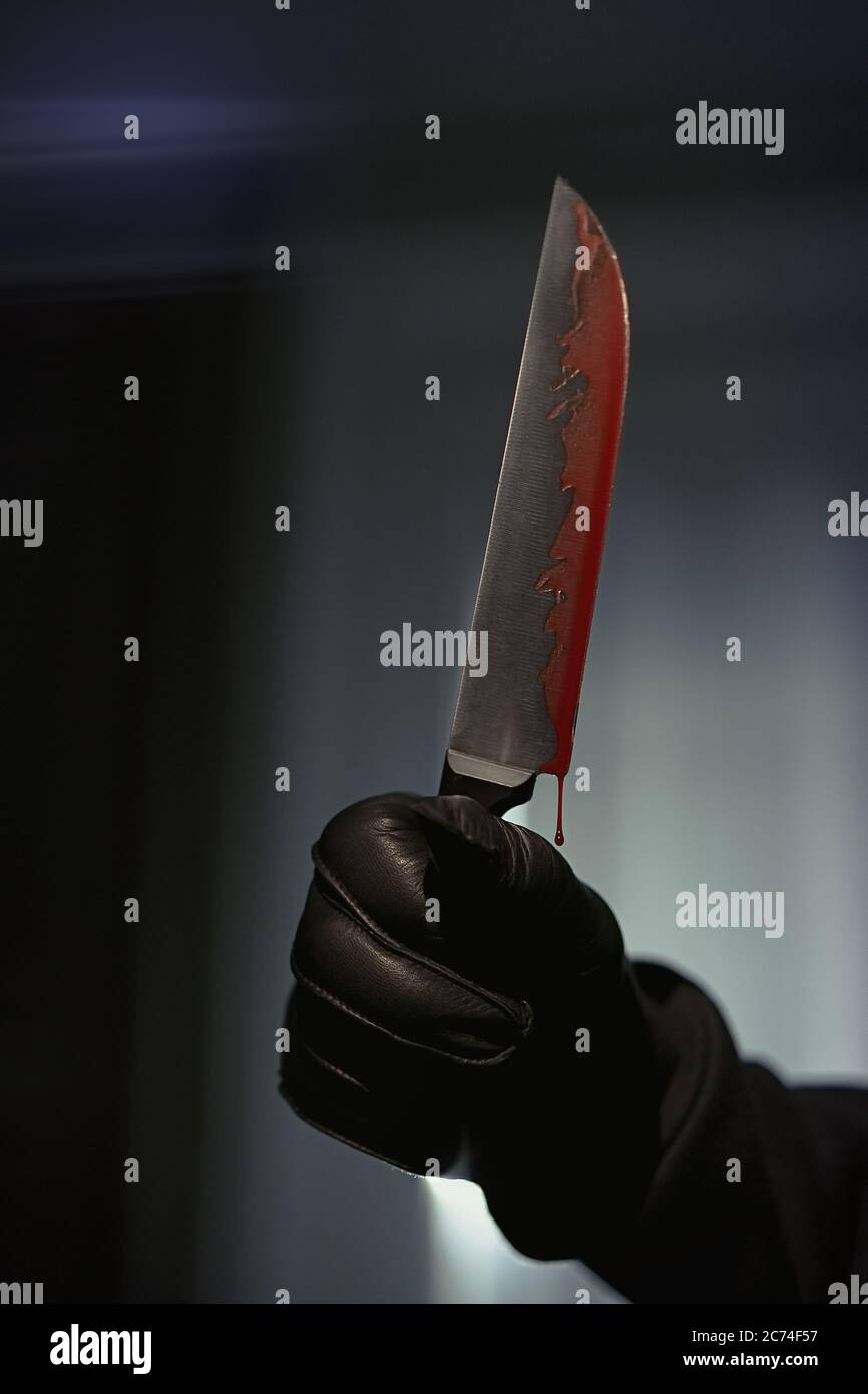 A man with a bloody knife standing in apartment, hands leather gloves ...