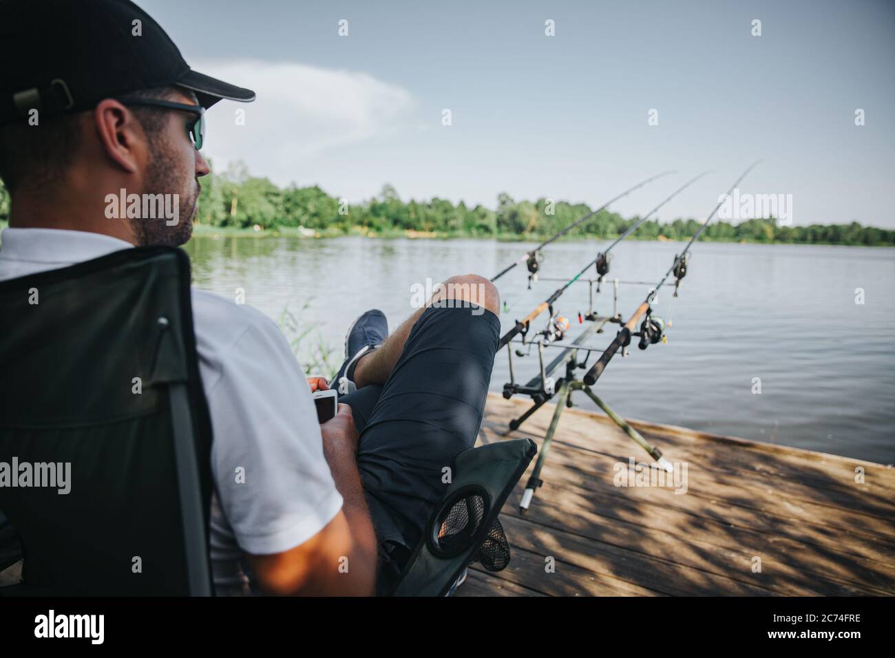 Young fisherman fishing on lake or river. Guy sitting in folding chair ...