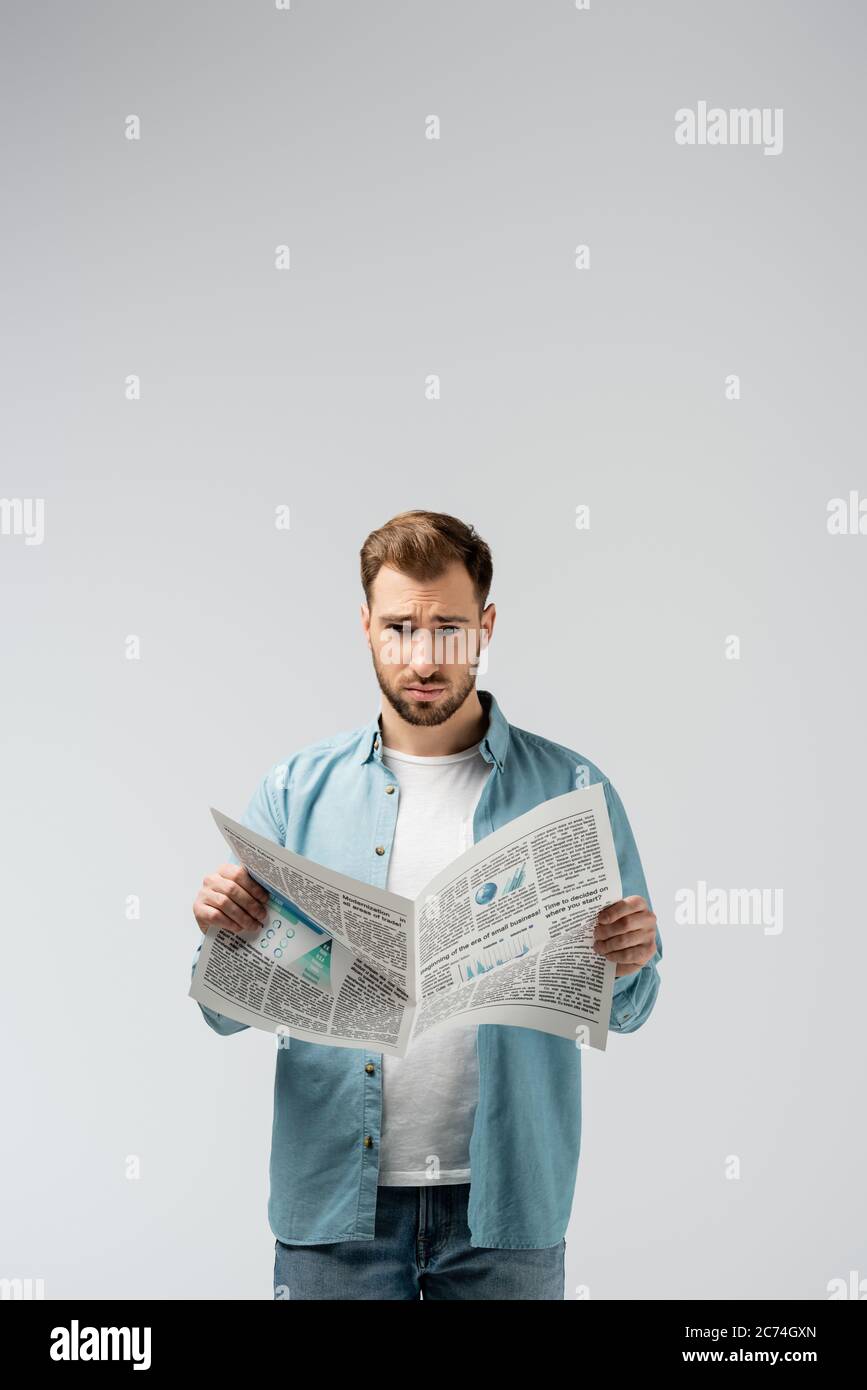 confused young man reading newspaper isolated on grey Stock Photo - Alamy