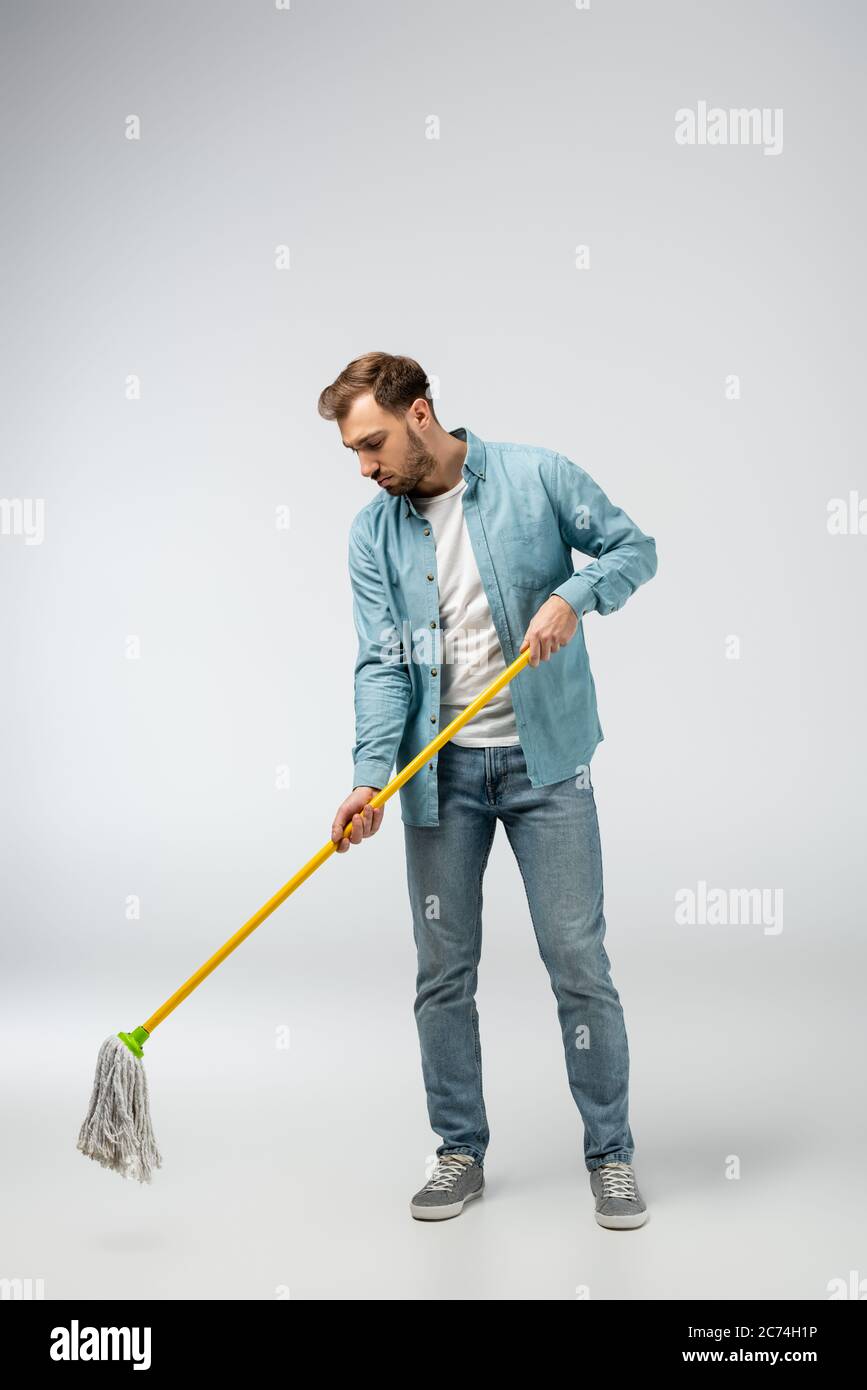 sad young man cleaning floor with mop isolated on grey Stock Photo - Alamy