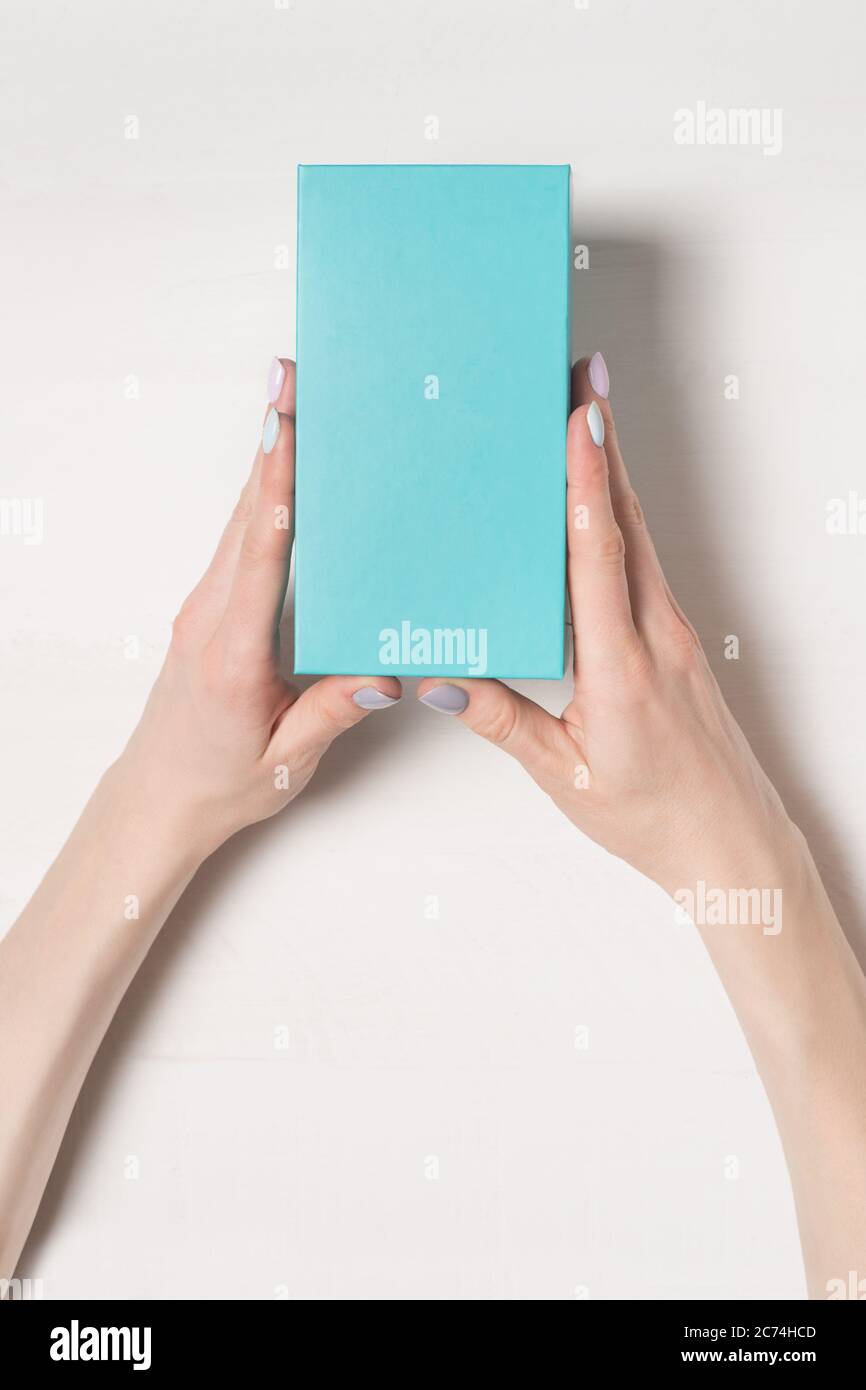 Rectangular turquoise box in female hands. Top view. White table on the ...