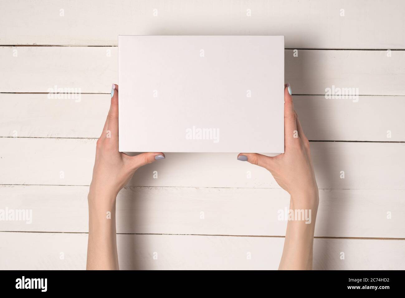 White rectangular box in female hands. Top view. White table on the ...