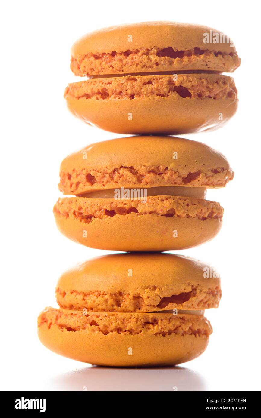 Three orange flavoured macaroons standing on top of each other on white ...