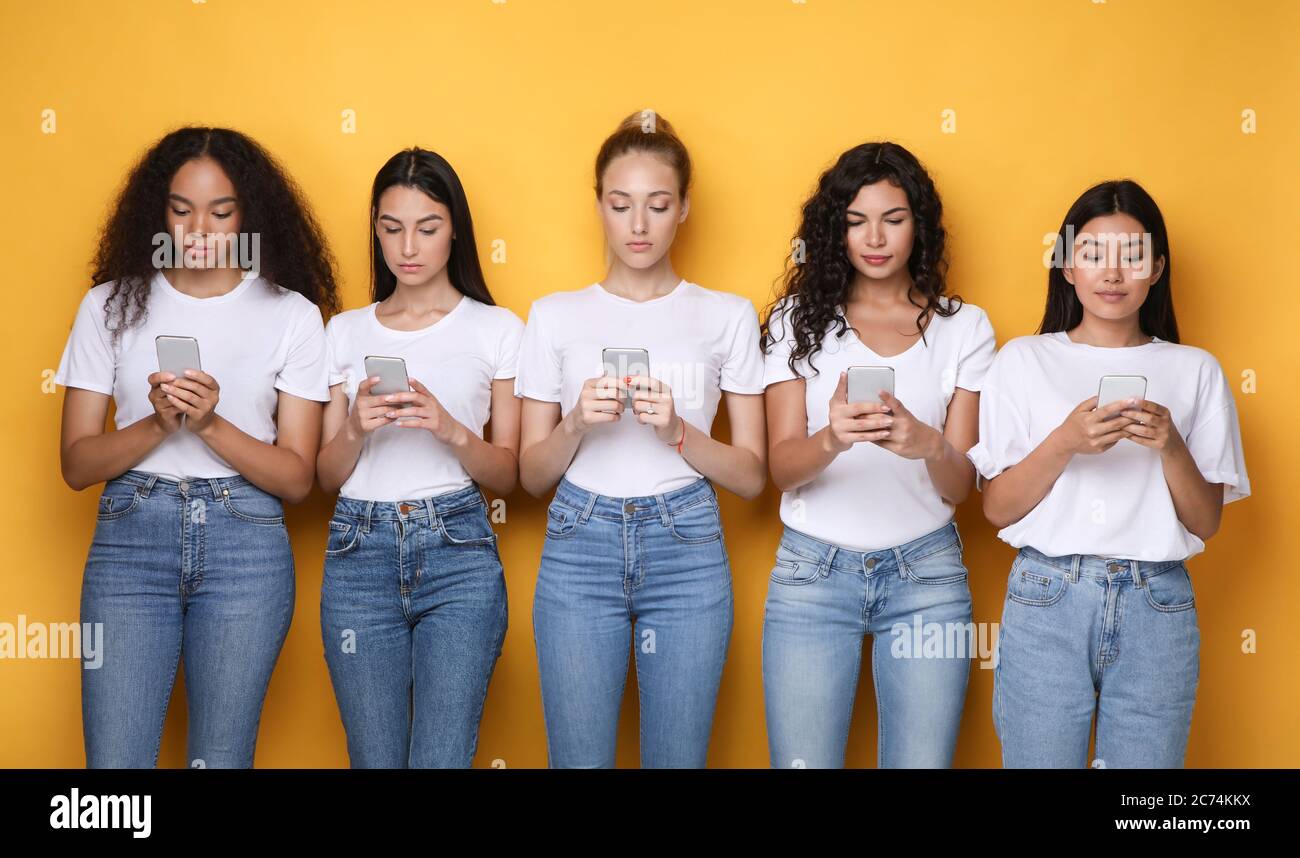 Diverse Girls Using Smartphones Texting Standing Over Yellow Background ...