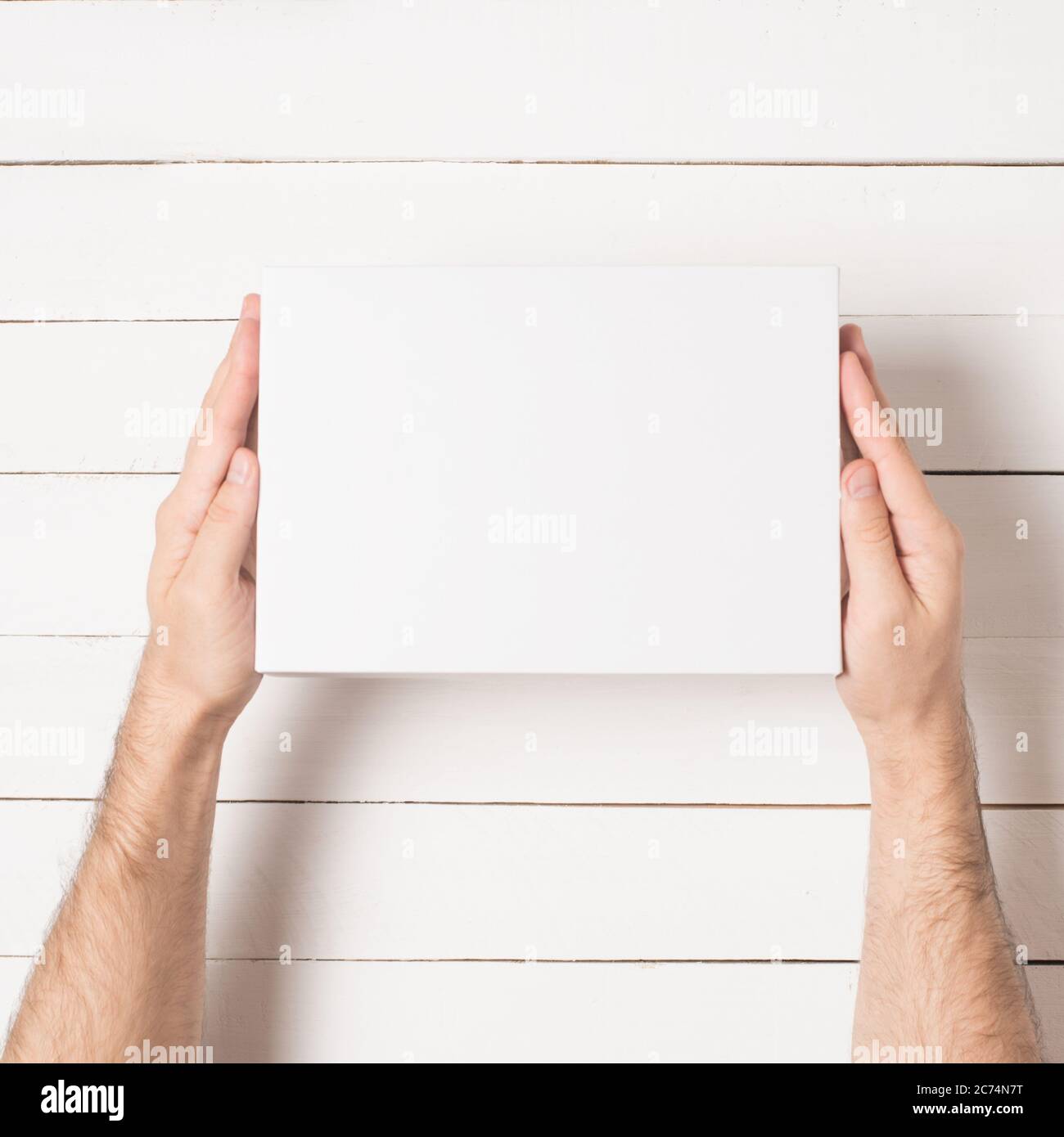 White rectangular box in male hands. Top view. White table on the ...