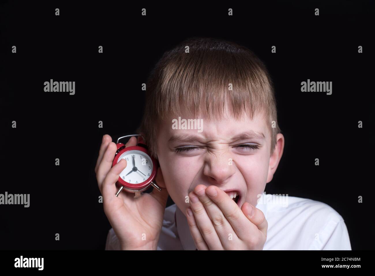 Yawning schoolboy with a red alarm clock in his hands. Morning concept ... Yawning schoolboy with a red alarm clock in his hands. Morning concept ...