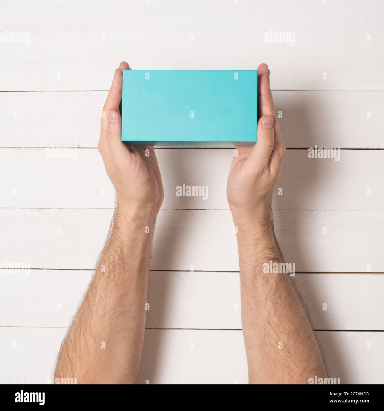 Rectangular turquoise box in male hands. Top view. White table on the ...