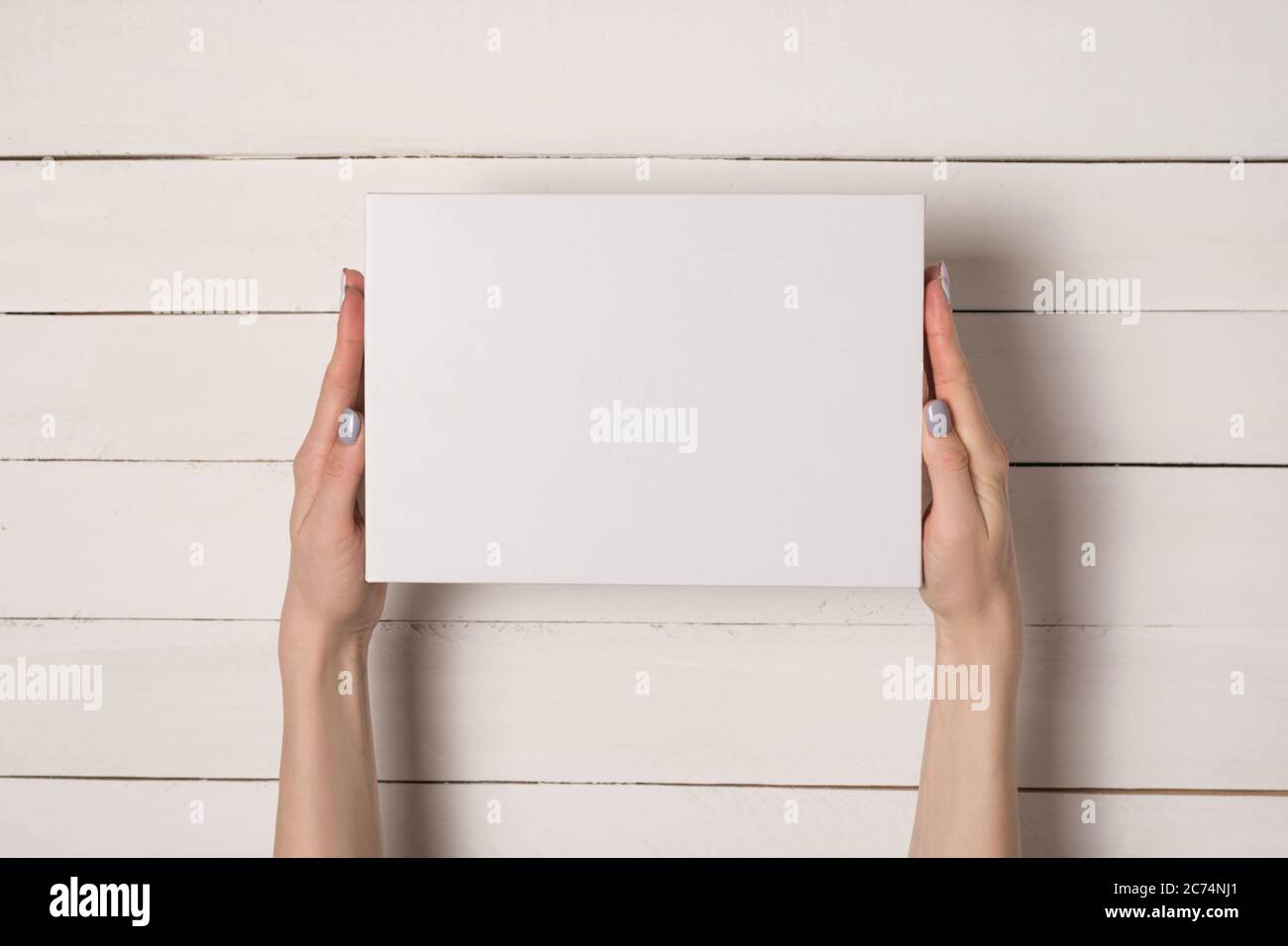 White rectangular box in female hands. Top view. White table on the ...