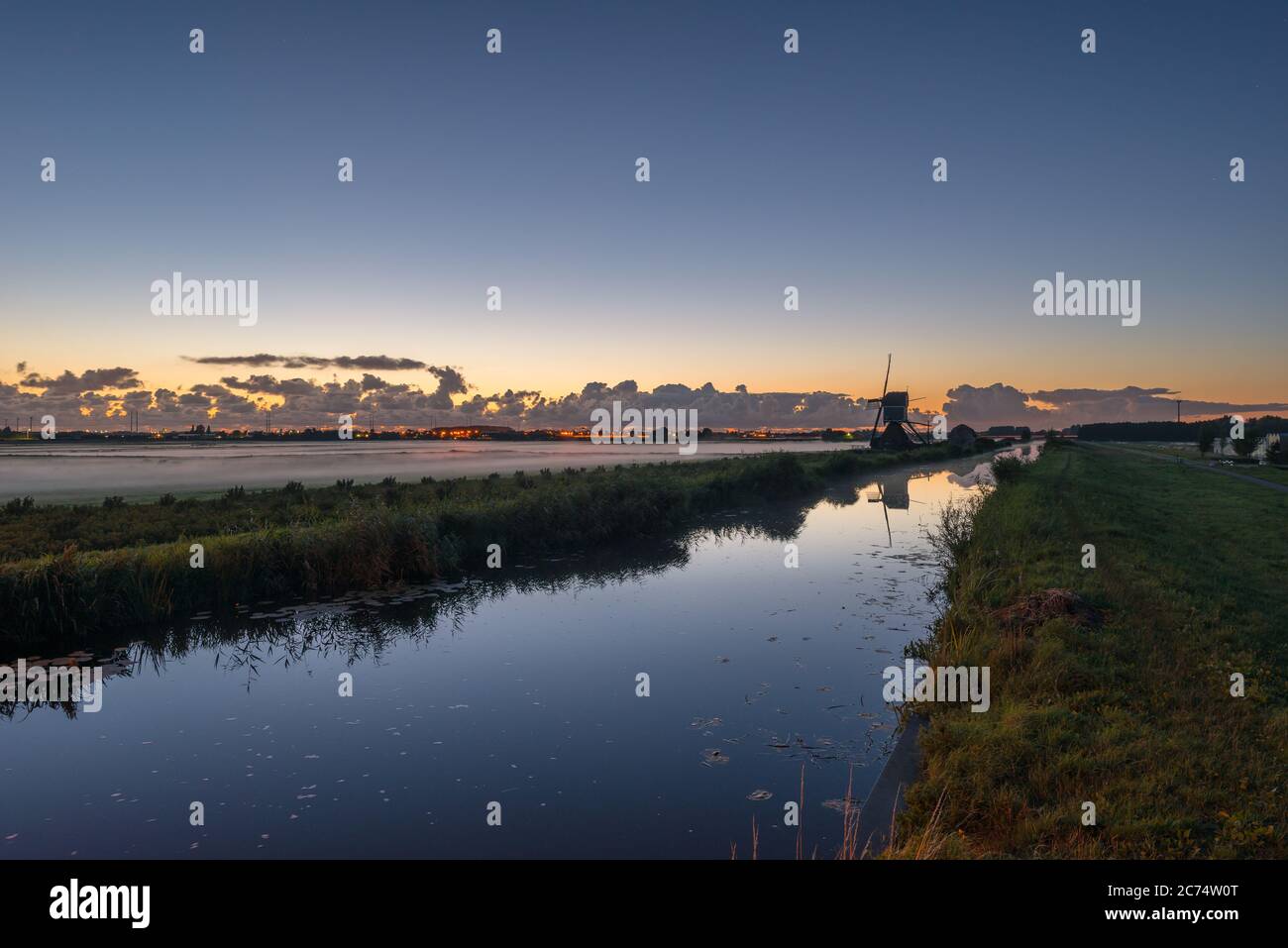 Typical dutch scene after sunset with windmill along the waterside and ...