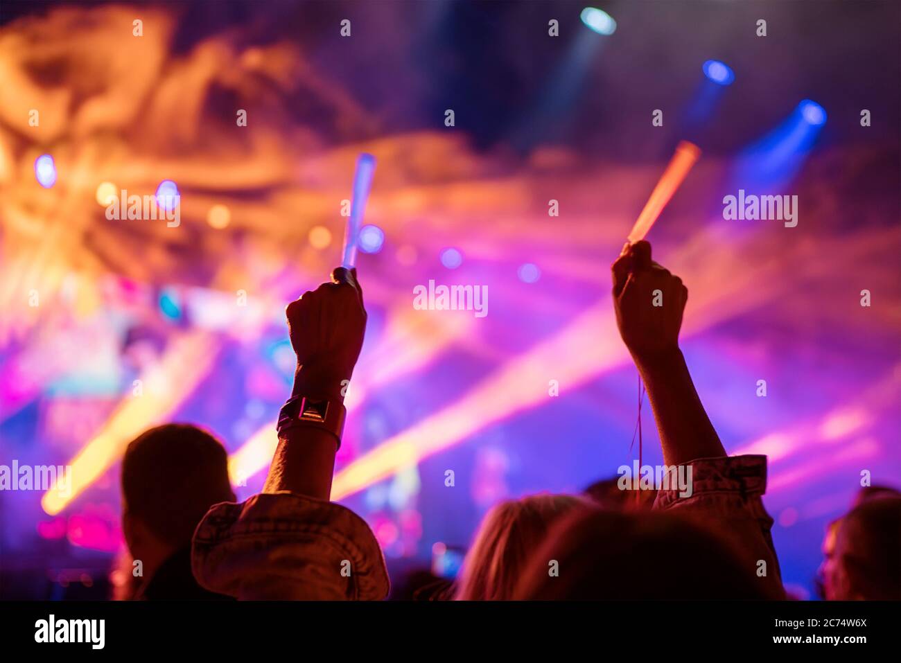 Young teenager girl fan raised up two hands with colored glowing sticks ...