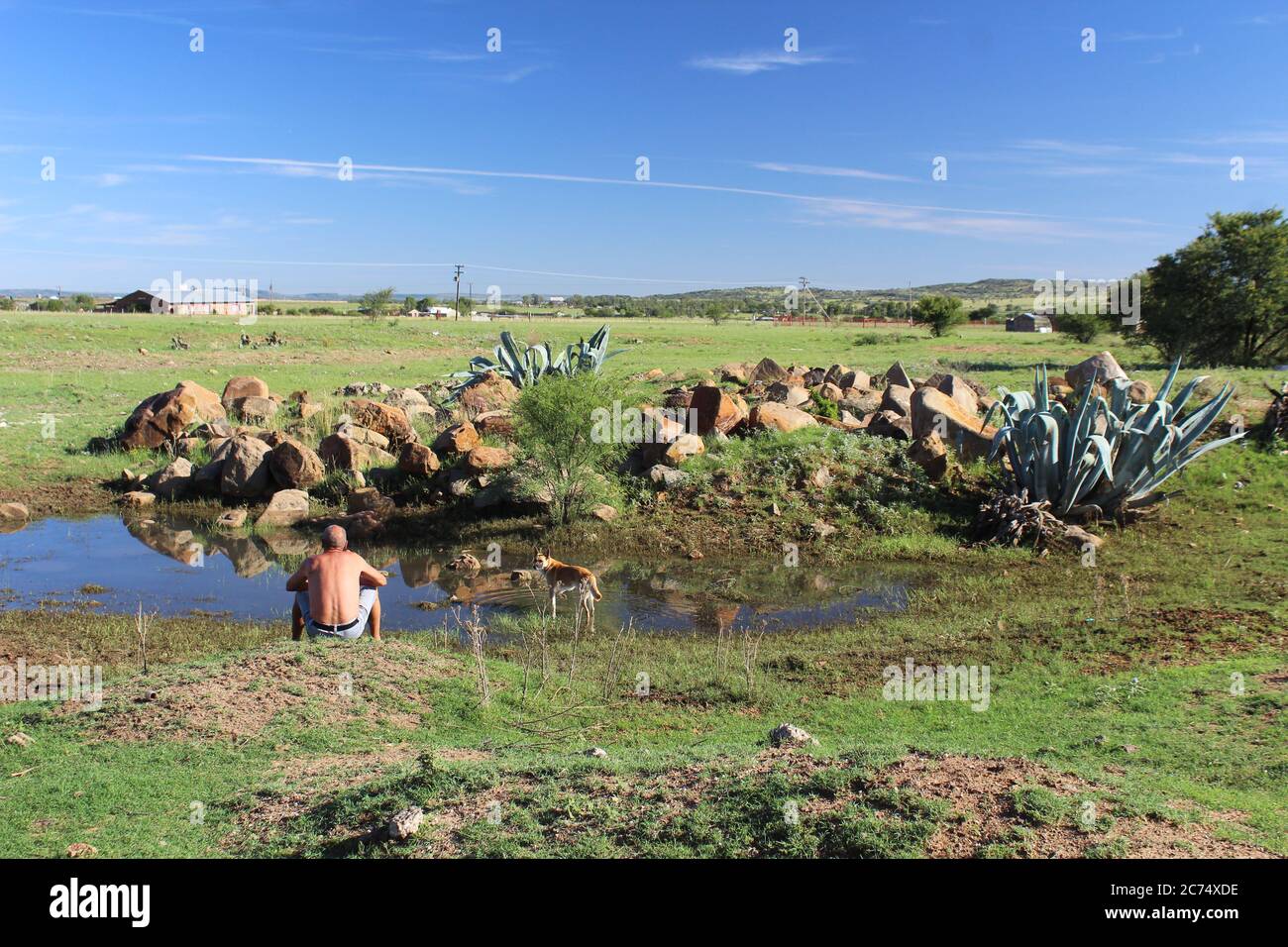 Man sitting at a small dam in African landscape Stock Photo - Alamy