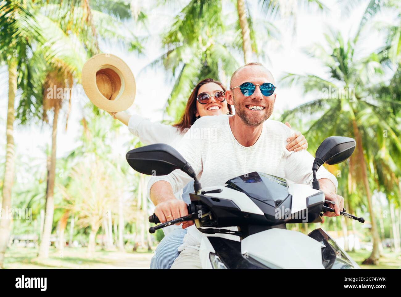 Laughing happy couple travelers riding motorbike during their tropical ...