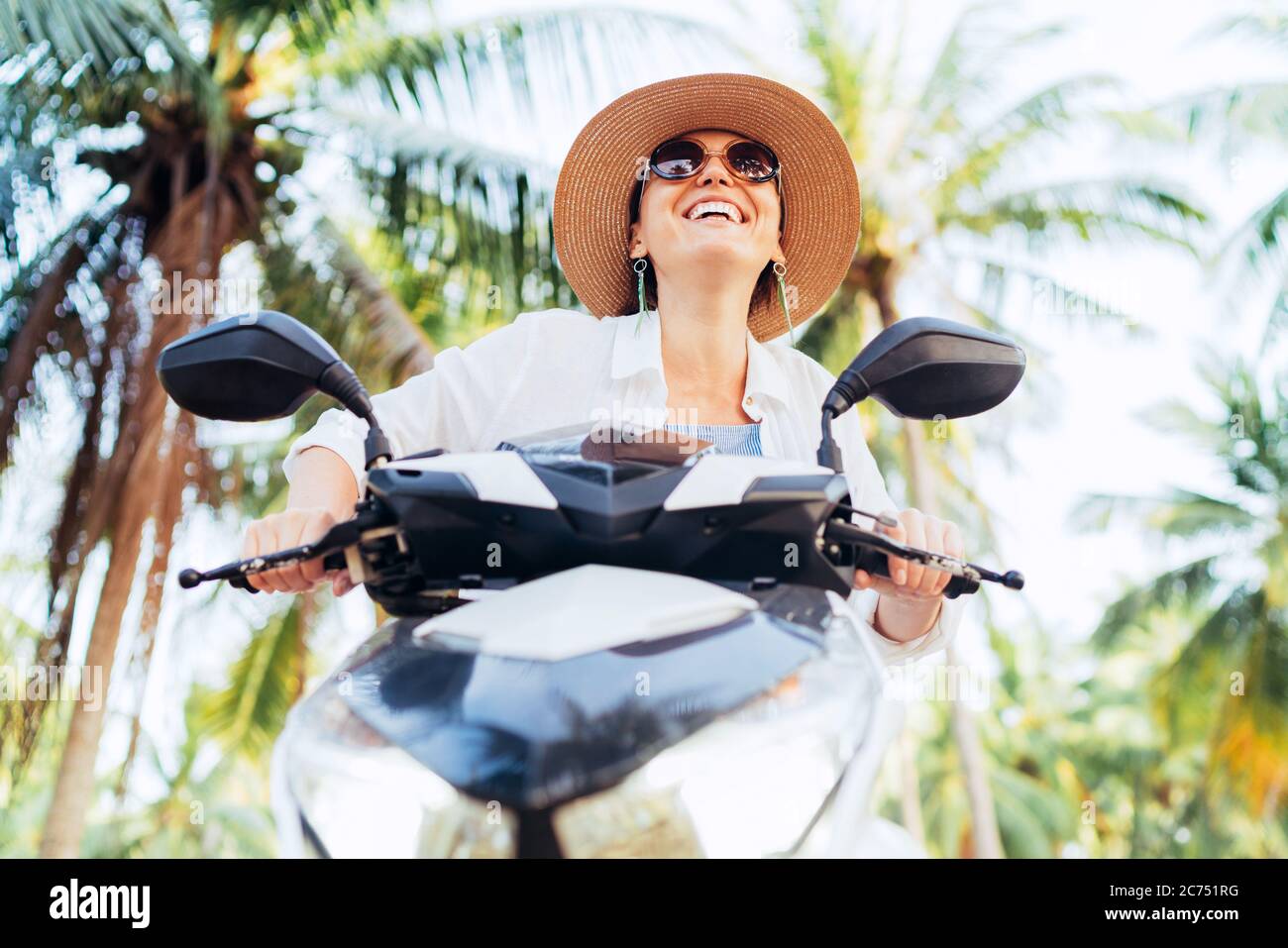 Happy smiling traveller woman riding Scooter motorbike under palm trees ...