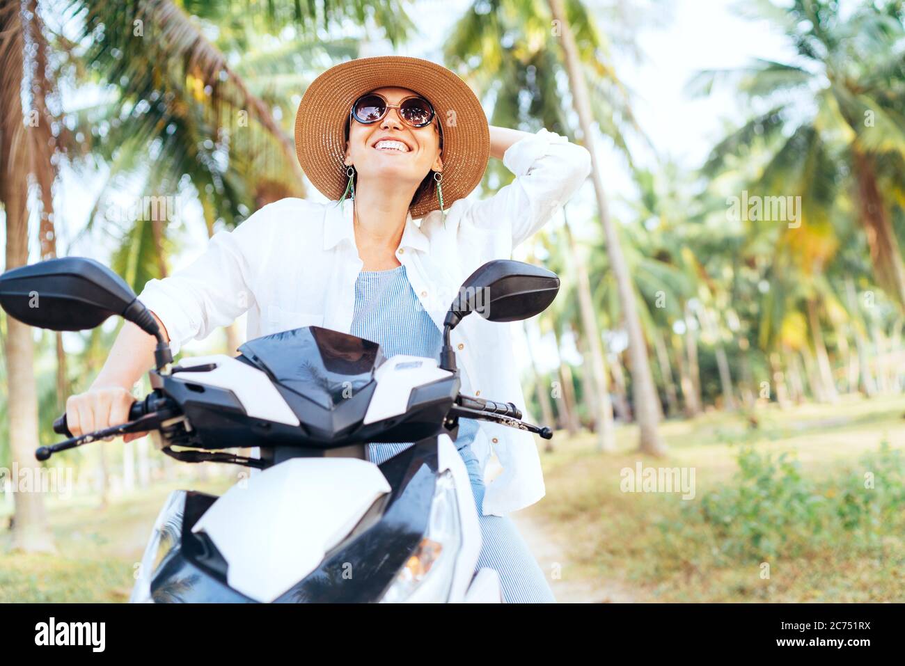 Happy smiling traveller woman riding Scooter motorbike under palm trees ...