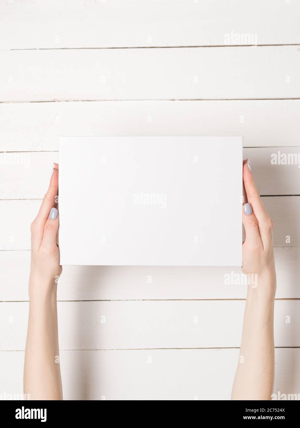 White rectangular box in female hands. Top view. White table on the ...