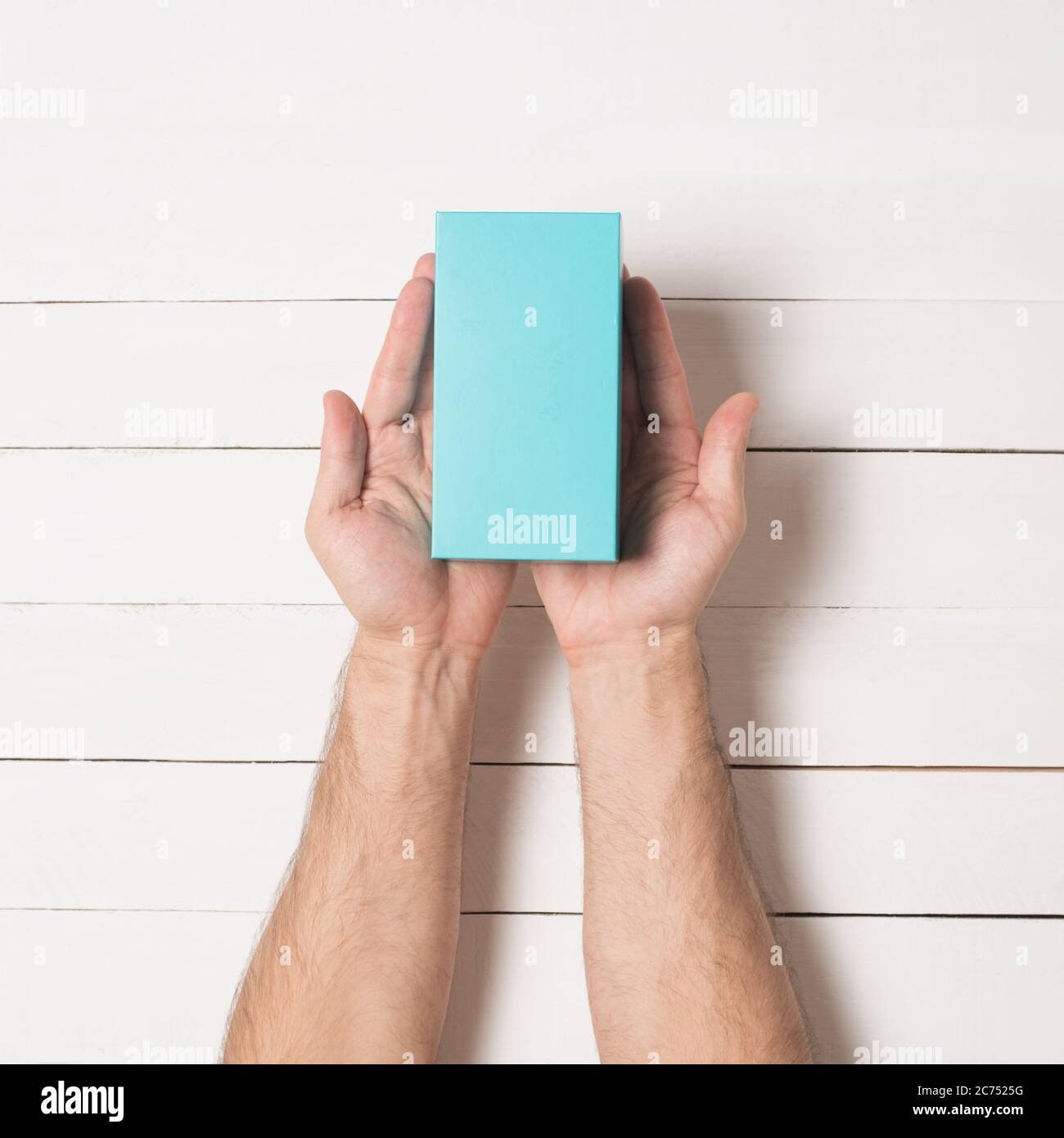 Rectangular turquoise box in male hands. Top view. White table on the ...