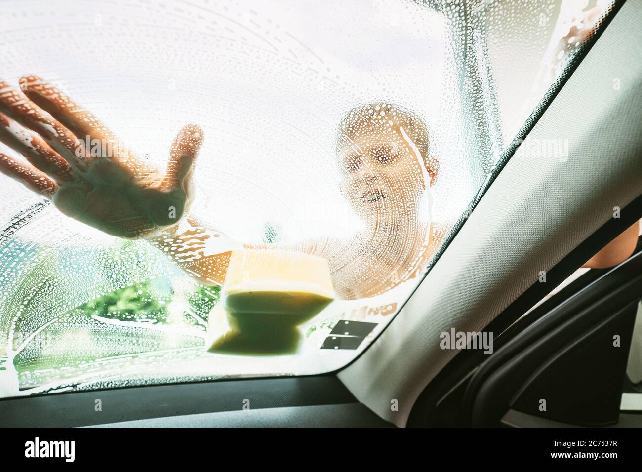 Little Boy washing his family windshield car window with soap foamy ...