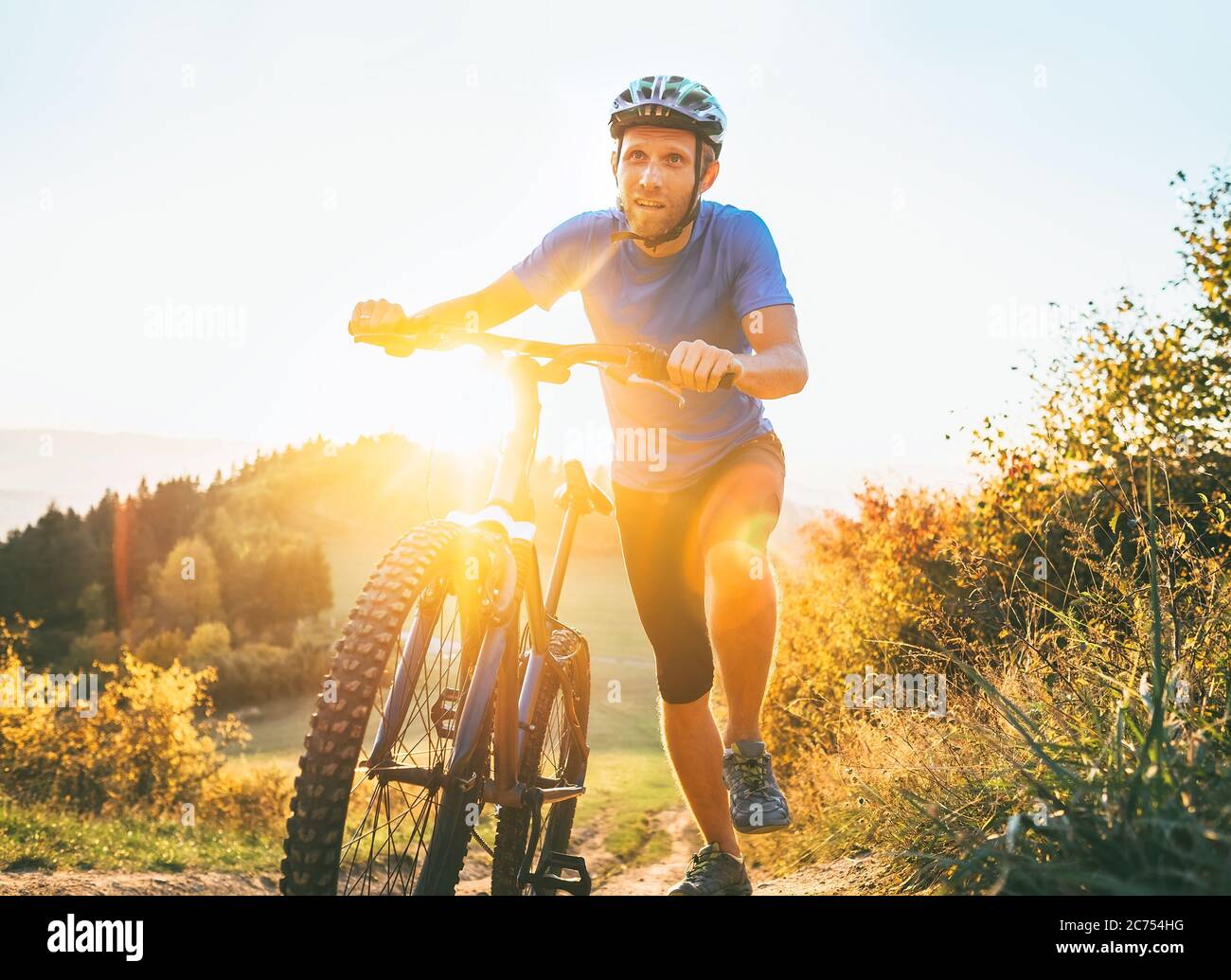 Young smiling man pushing a mountain bike up the hill. Active adventure ...