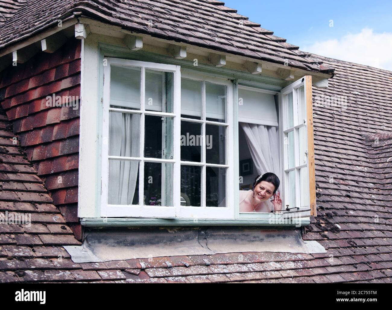 Woman in forties opening and looking out an open window with multi pane ...