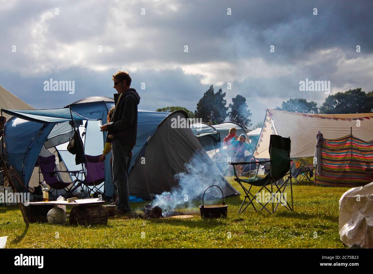 Preparing to cook on a campfire at a festival campsite with dark storm ...