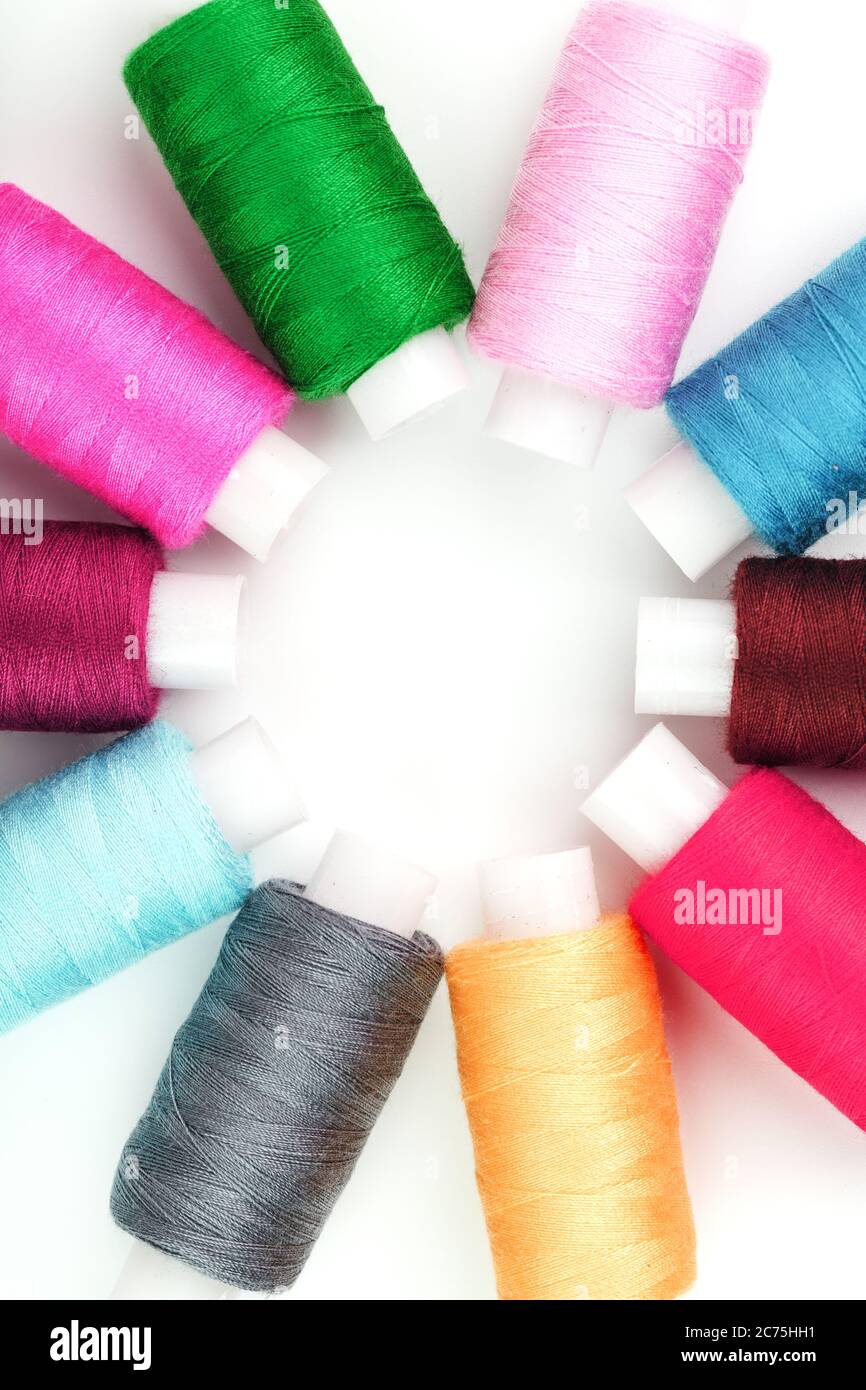 Sewing threads of different colors on reels on a white background in a ...