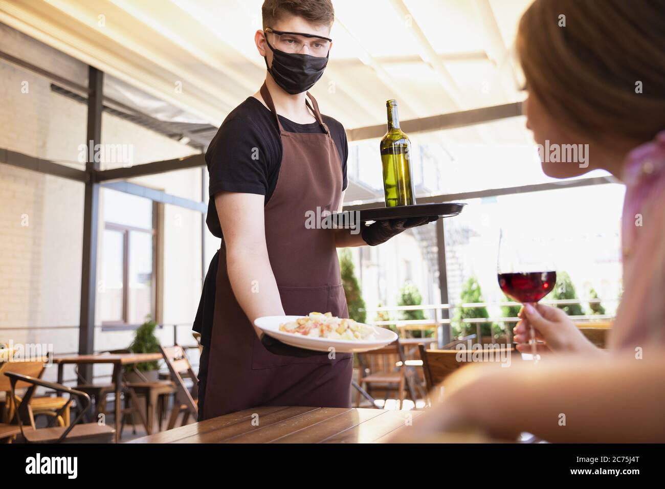 The waiter works in a restaurant in a medical mask, gloves during ...