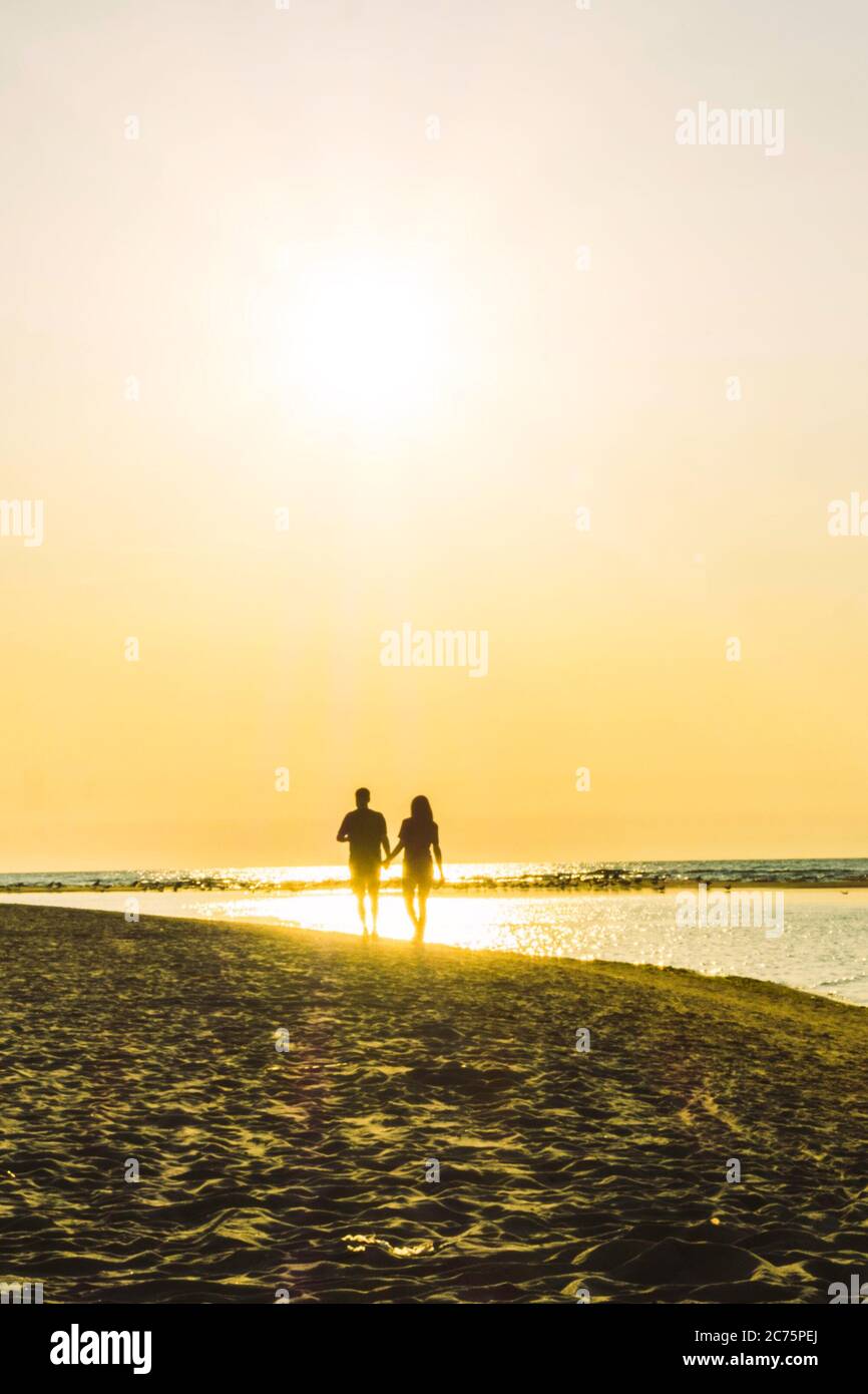 Two People Walking On The Beach In The Sunset