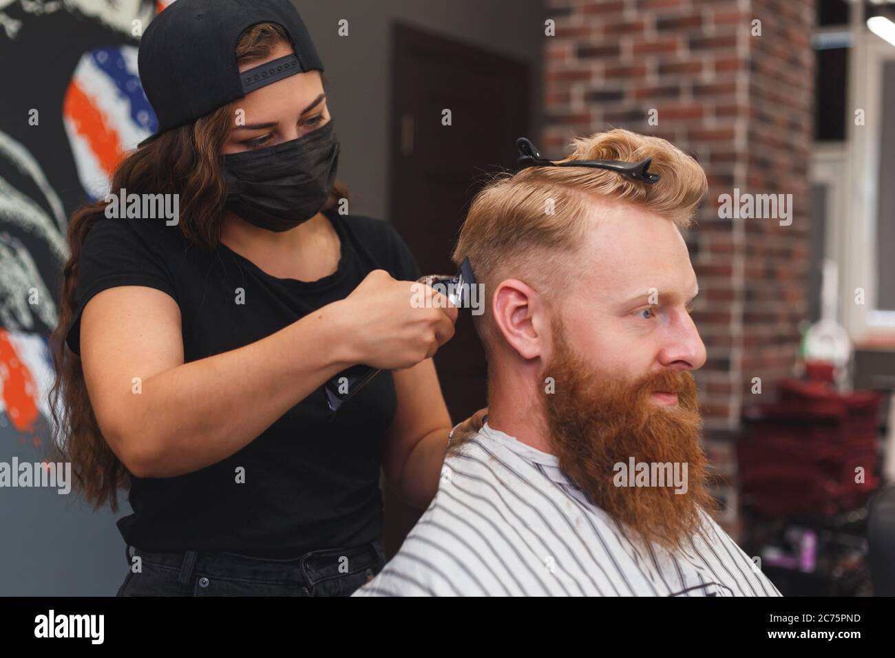Female barber in mask cuts a man hairs with hair clipper. hairstyle ...