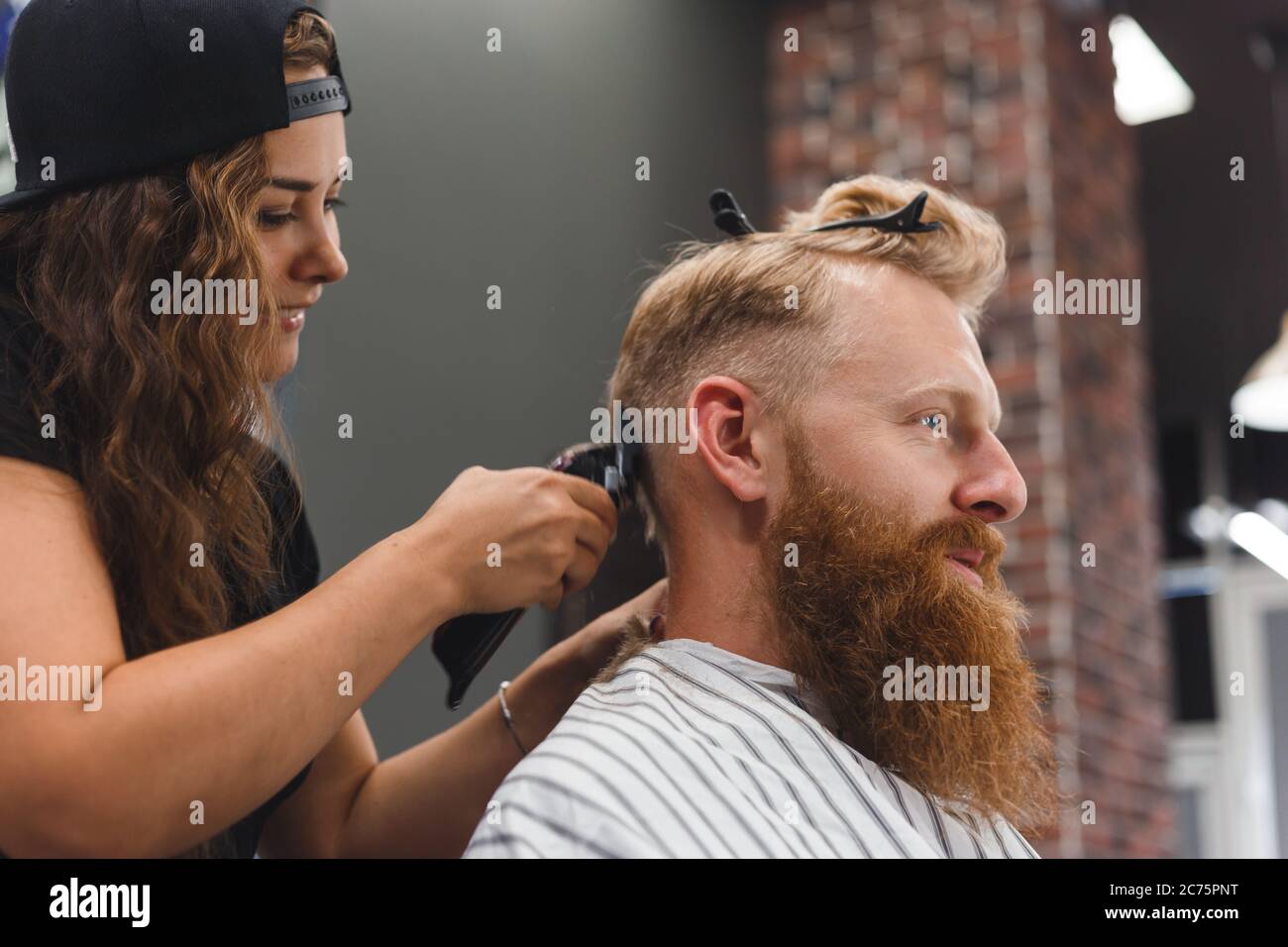 Female barber in mask cuts a man hairs with hair clipper. hairstyle ...