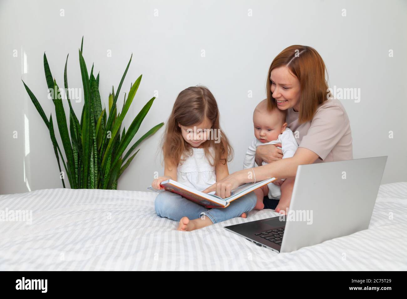 Mother with baby helping little girls doing homework with laptop, child ...