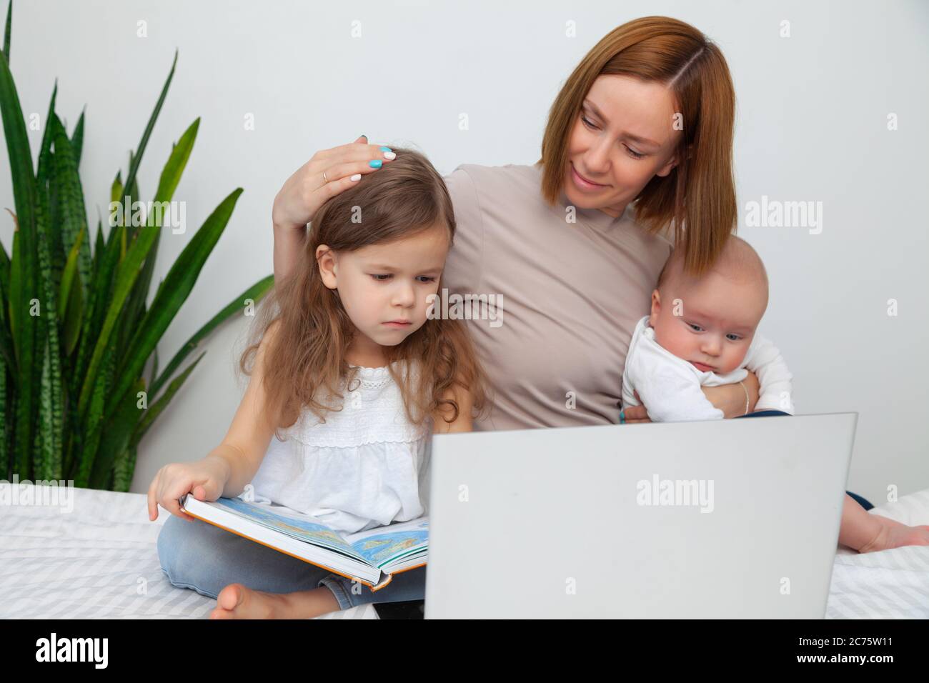 Mother with baby helping little girls doing homework with laptop, child ...
