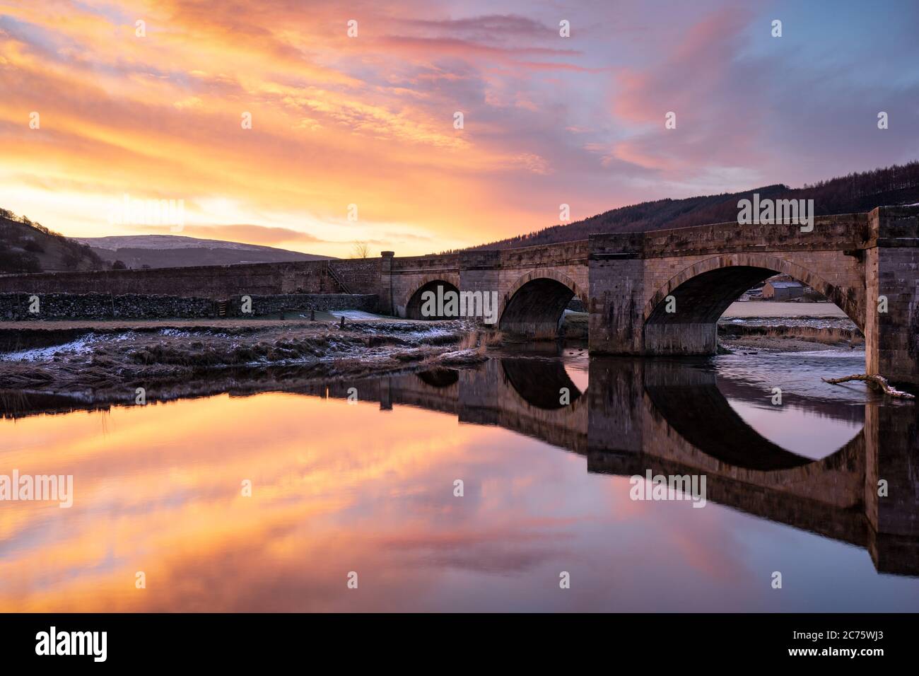 A vibrant sunrise highlights the arches of Burnsall Bridge in The ...