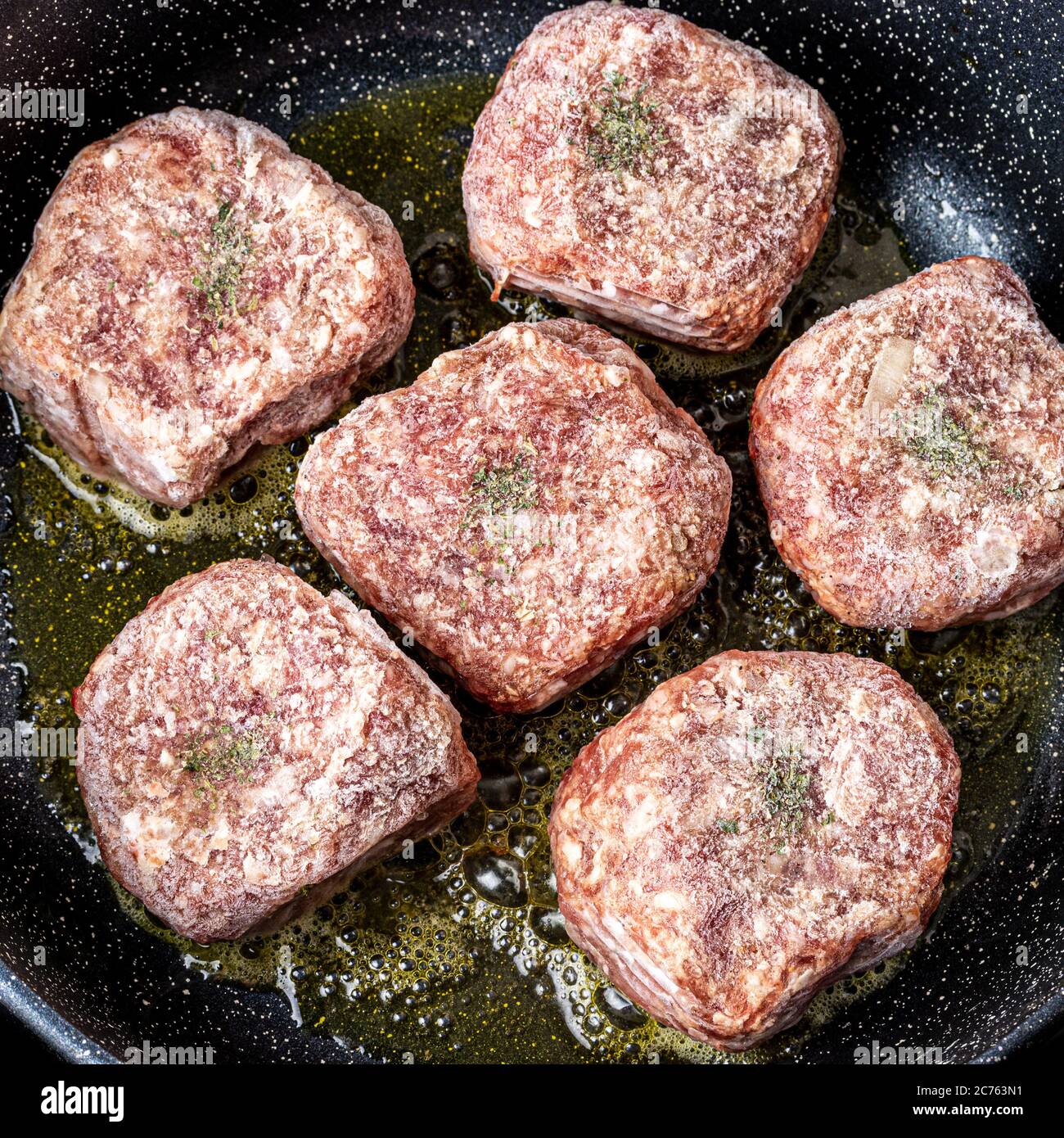 Raw beef cutlets, heated in a ceramic black skillet with vegetable oil ...