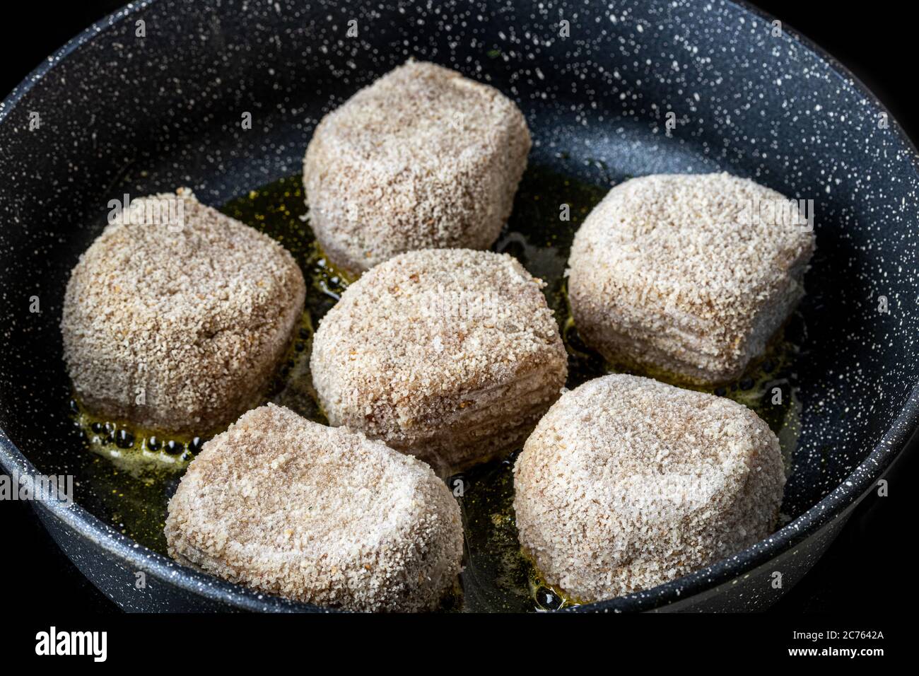 Raw frozen breaded chicken cutlets, heated in a ceramic black skillet ...