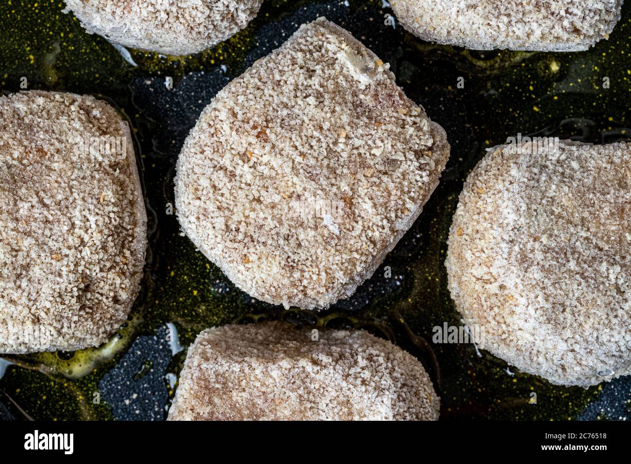 Raw frozen breaded chicken cutlets, heated in a ceramic black skillet ...