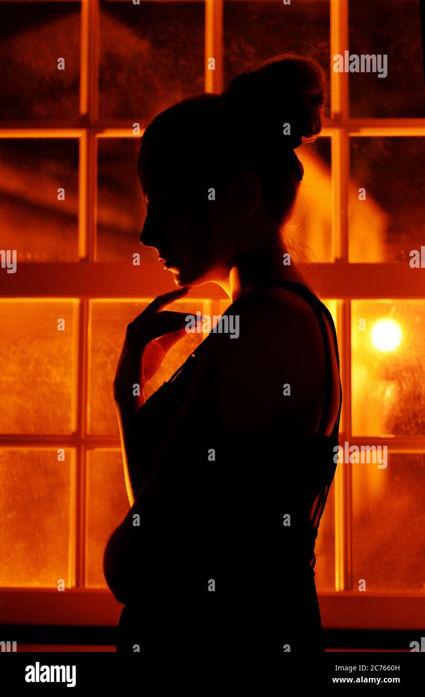 elegant young woman standing by the window at night Stock Photo - Alamy