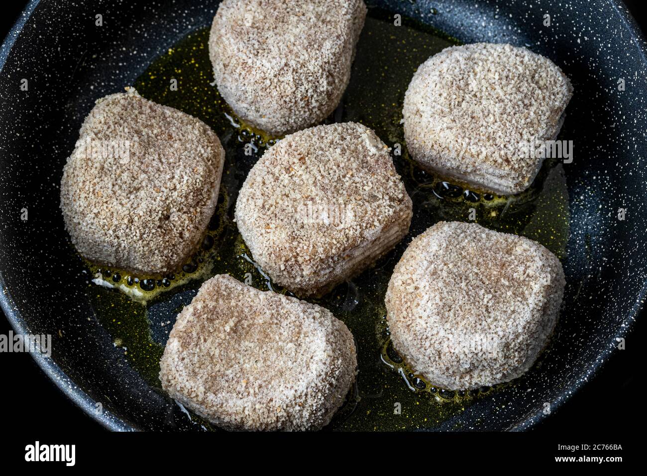 Raw frozen breaded chicken cutlets, heated in a ceramic black skillet ...