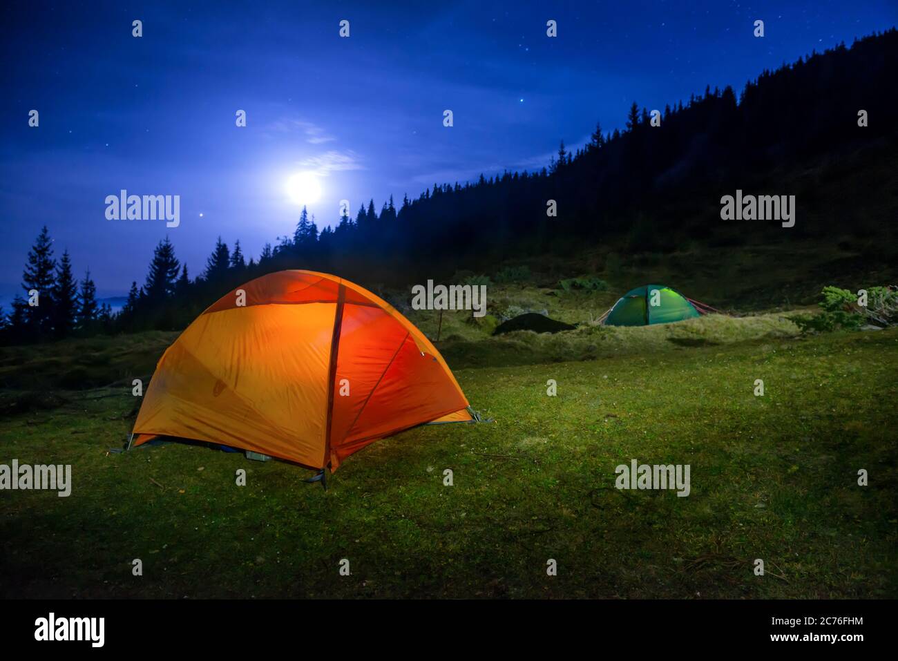 Two Illuminated orange and green camping tents under moon, stars at ...