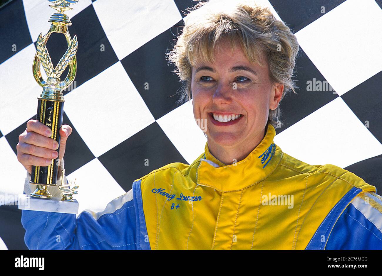 Blond female racing car driver poses with checkered flag and winning ...